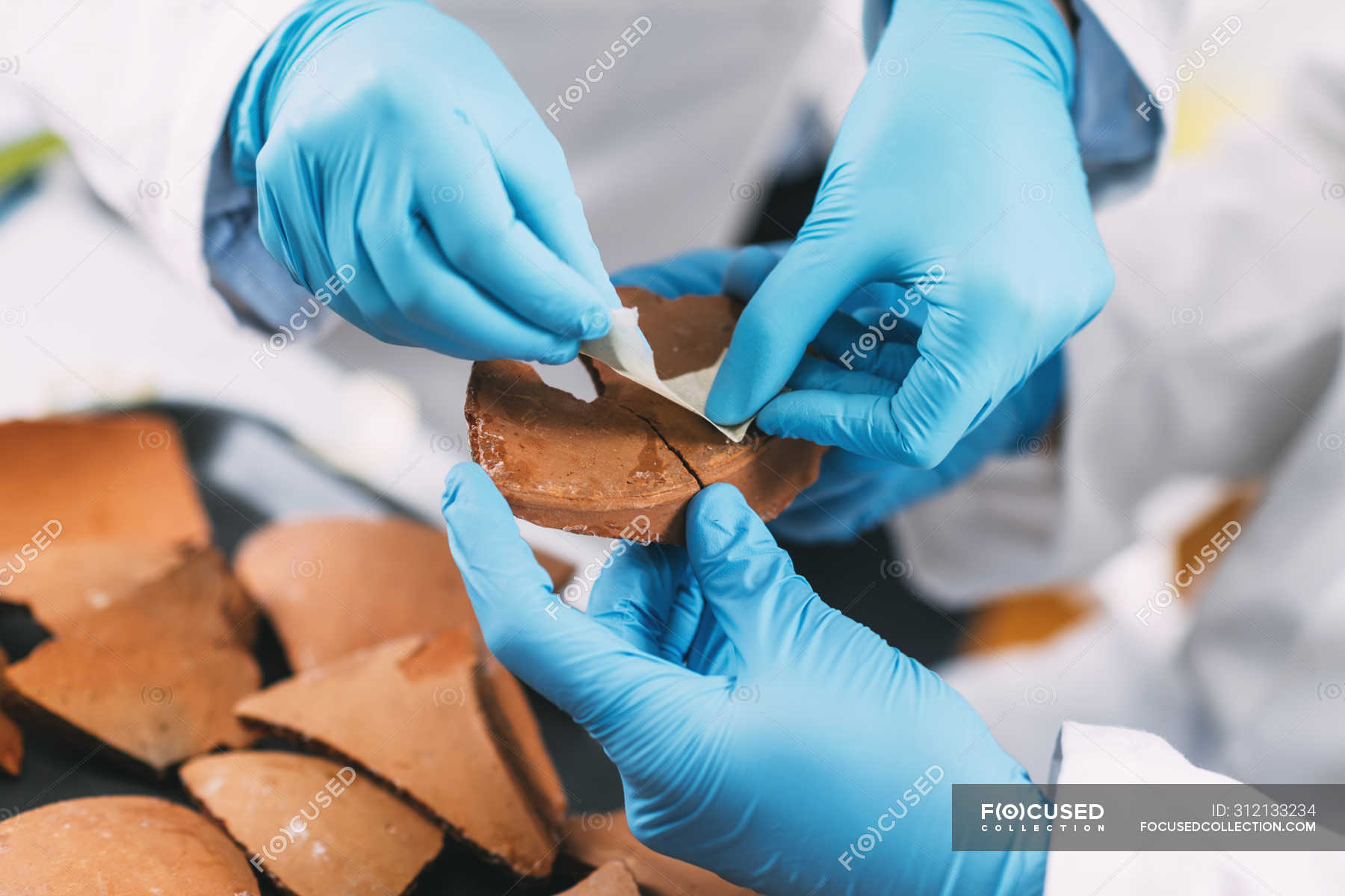 Hands of archaeologists reconstructing broken pottery in laboratory ...