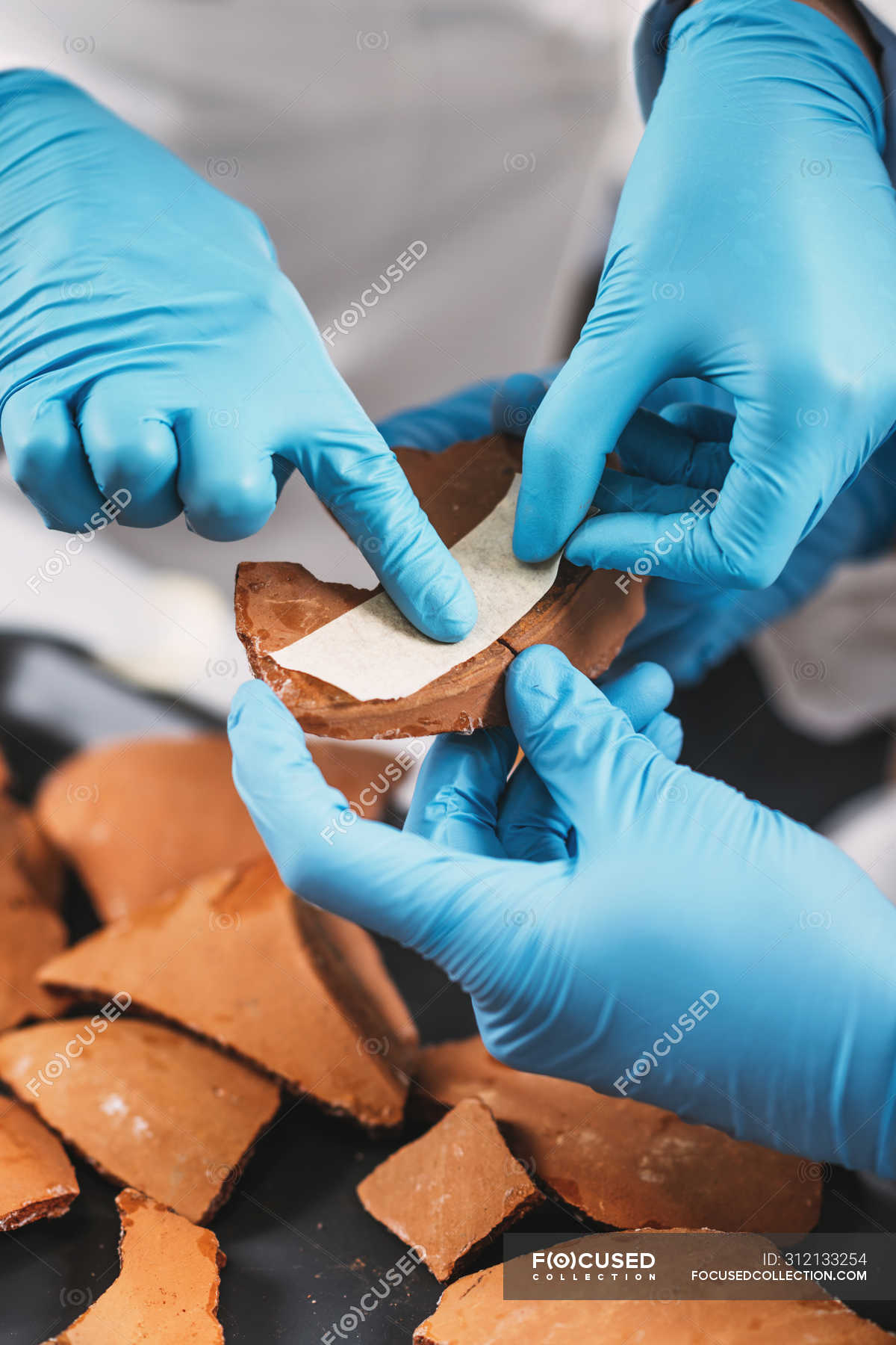 Hands of archaeologists reconstructing broken pottery in laboratory ...