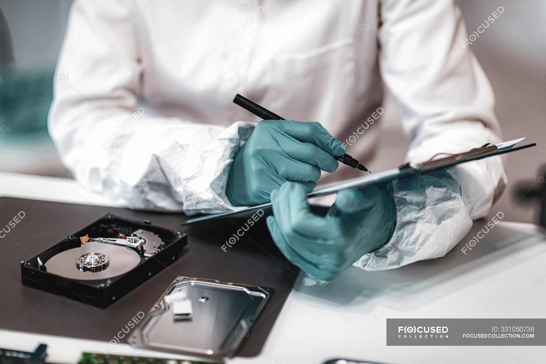 Forensic science technician taking notes while examining computer hard ...
