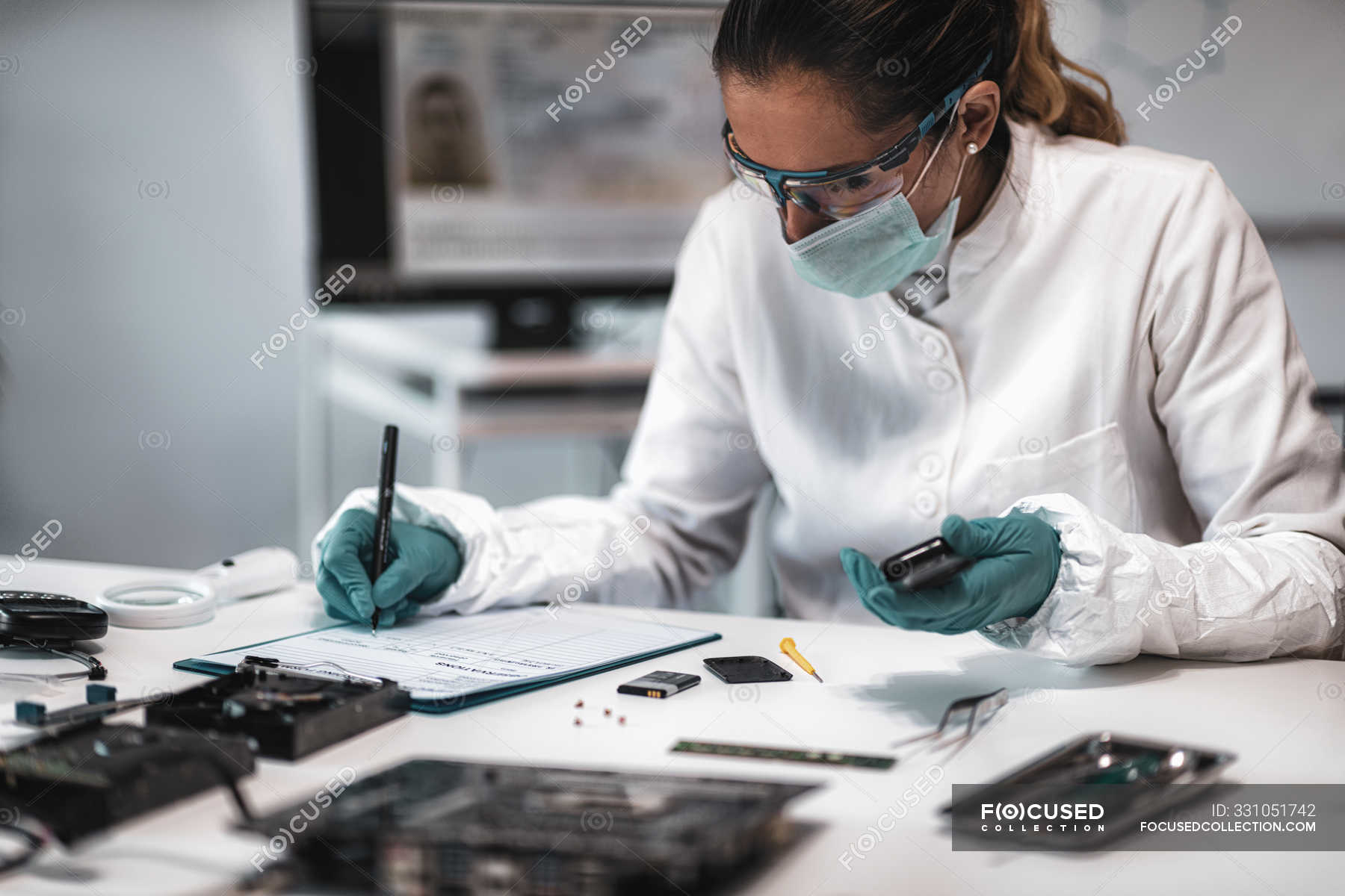 Police forensic analyst taking notes while examining confiscated mobile ...