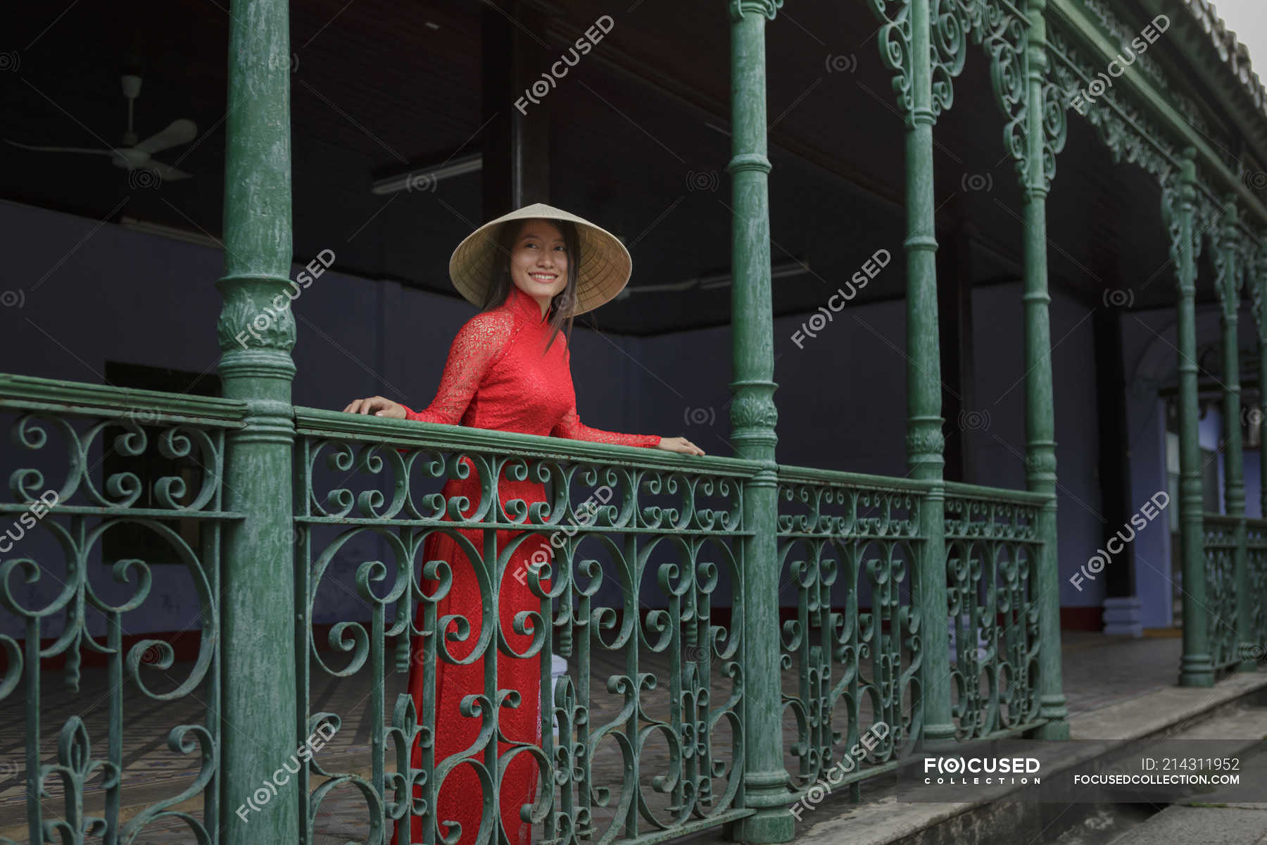 Vietnamese woman wearing conical hat standing on a balcony in Hoi An in her Ao Dai — person, red ...