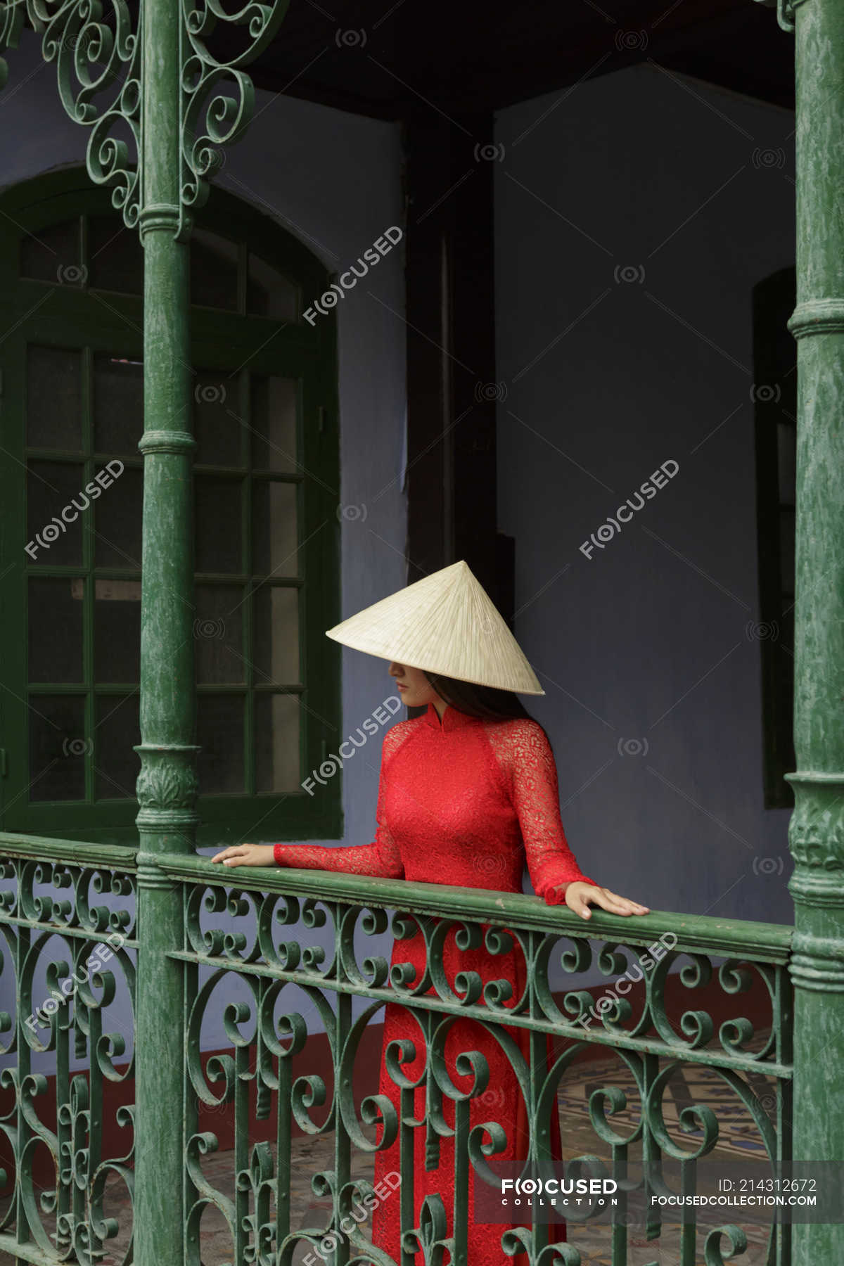 Vietnamese woman wearing conical hat standing on a balcony in Hoi An in her Ao Dai — contrast ...