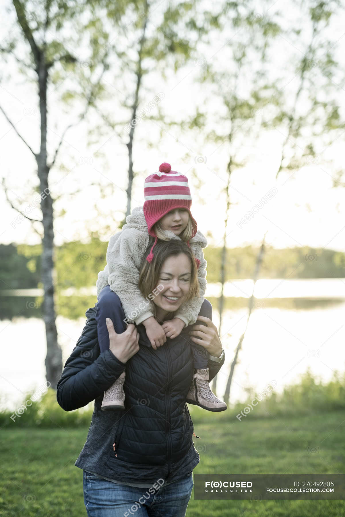 Mother carrying daughter piggyback at lake in nature — people, outdoors ... Mother carrying daughter piggyback at lake in nature — people, outdoors ...