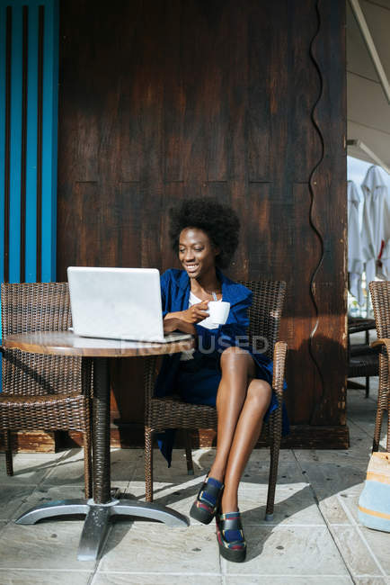 Young Woman With Laptop Sitting In A Street Cafe Drinking Coffee