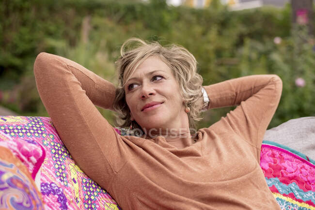 Smiling Woman Sitting With Hands Behind Head On Sofa At Back Yard