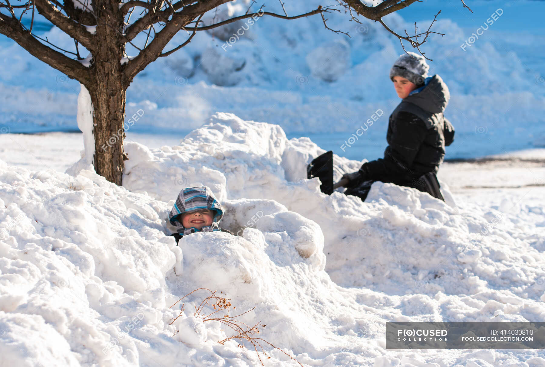 Two boys building snow forts with a shovel on a sunny winter day ...