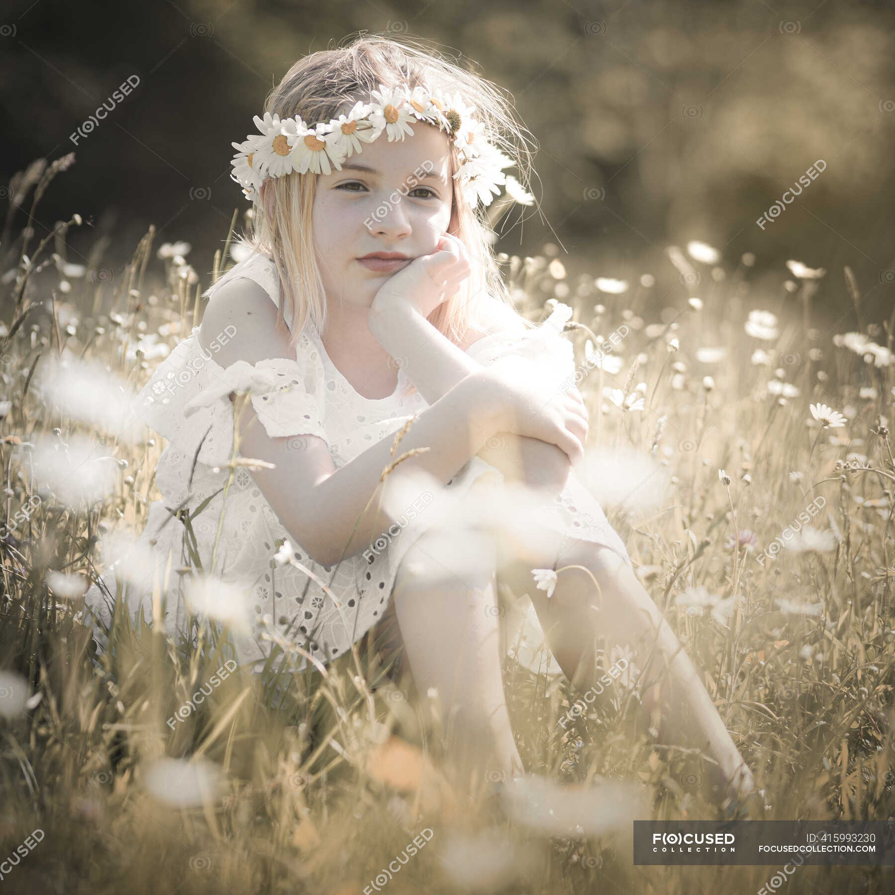 Girl with a melancholy look, sitting in a field with lots of flowers ...