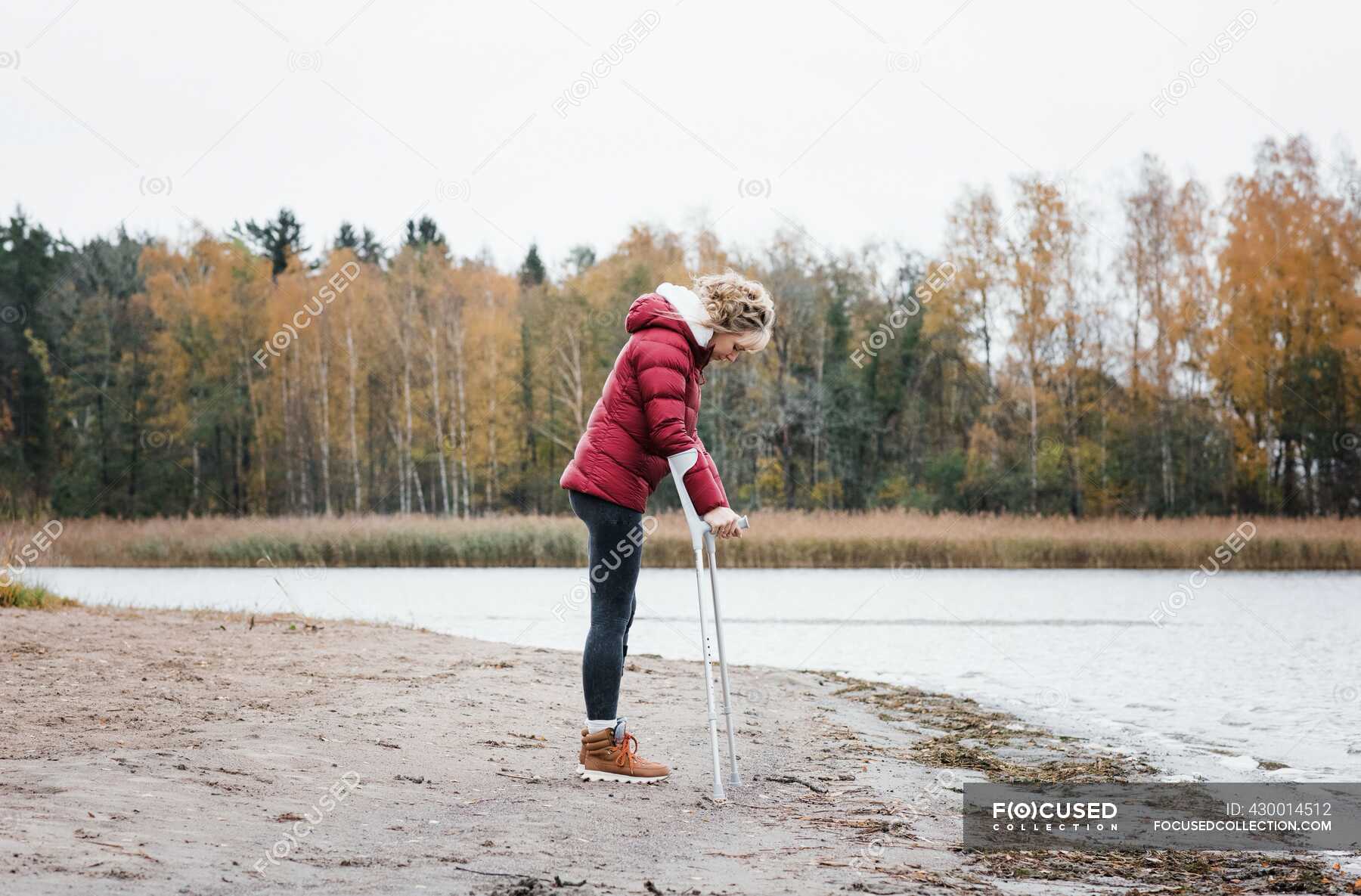 Injured woman stood at the beach with crutches looking thoughtful ...