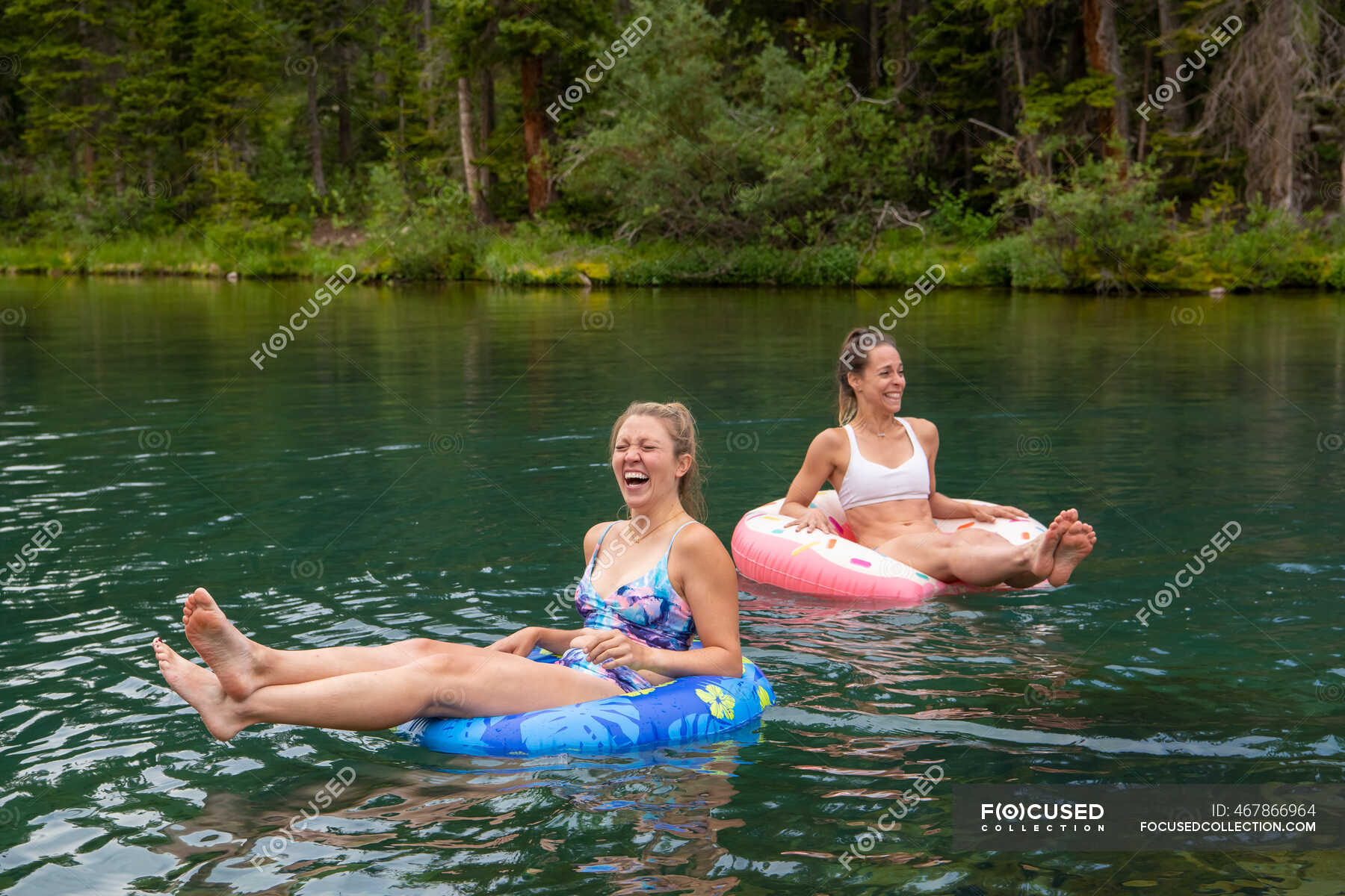 Cheerful female friends sitting on inflatable rings in lake — bonding ... Cheerful female friends sitting on inflatable rings in lake — bonding ...