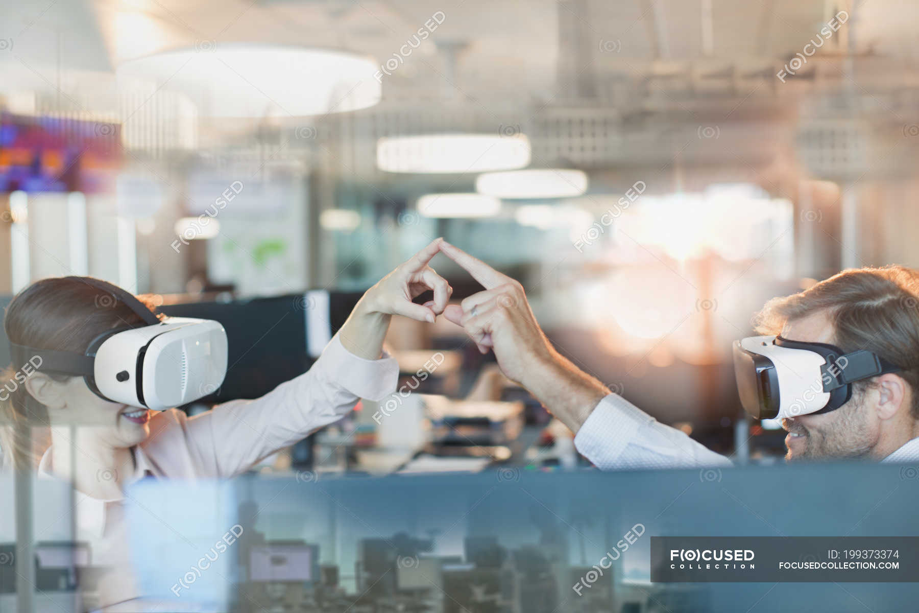 Computer programmers using virtual reality simulator glasses, touching fingers in office ...