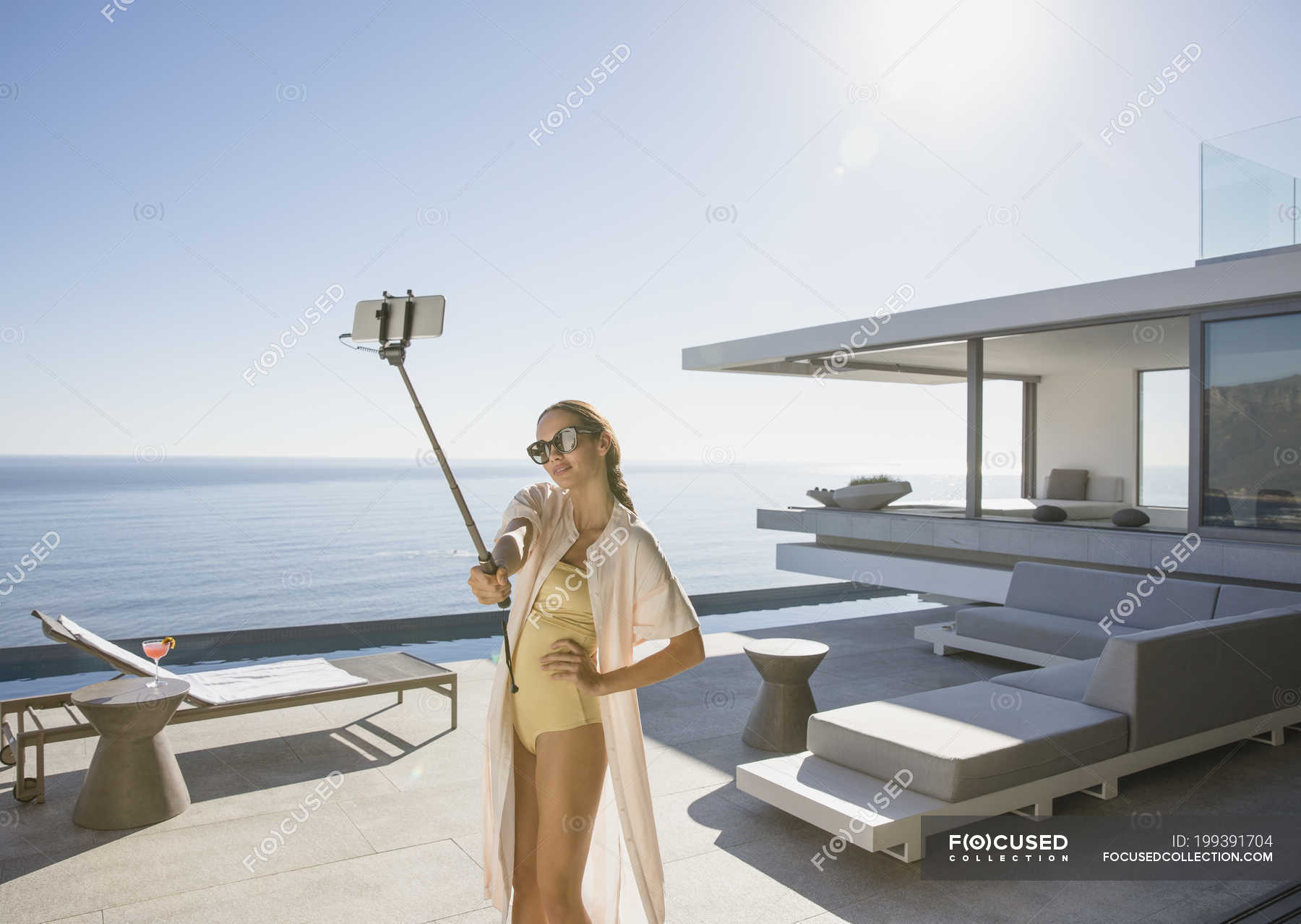 Woman In Bathing Suit Taking Selfie With Selfie Stick On Sunny Modern Luxury Home Showcase