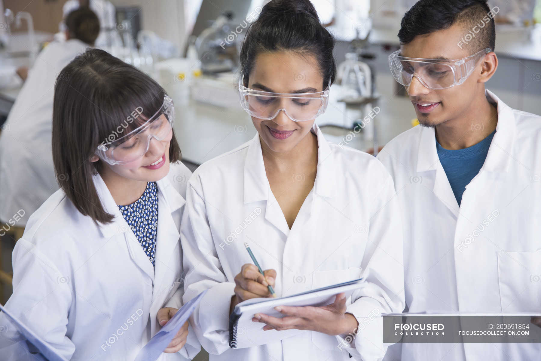 College students in lab coats discussing notes in science laboratory ... College students in lab coats discussing notes in science laboratory ...