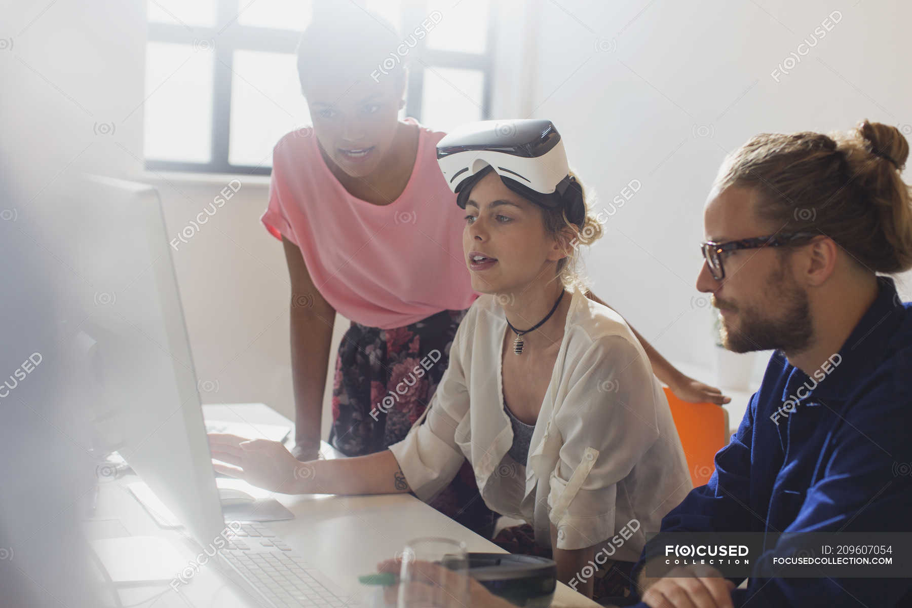 Computer programmers programming virtual reality simulator glasses at computer in office ...