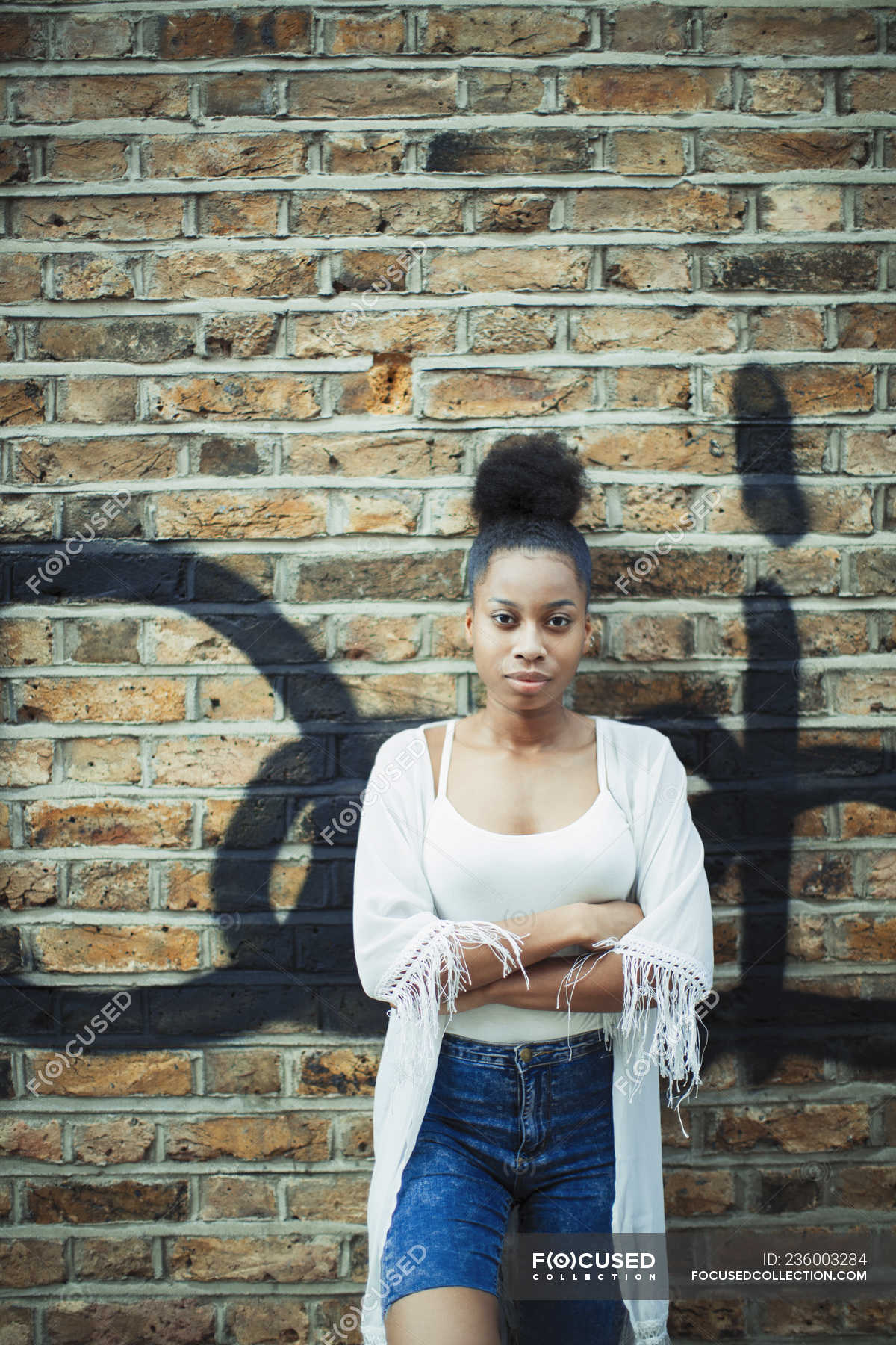 Portrait confident, serious young woman leaning against brick wall ...
