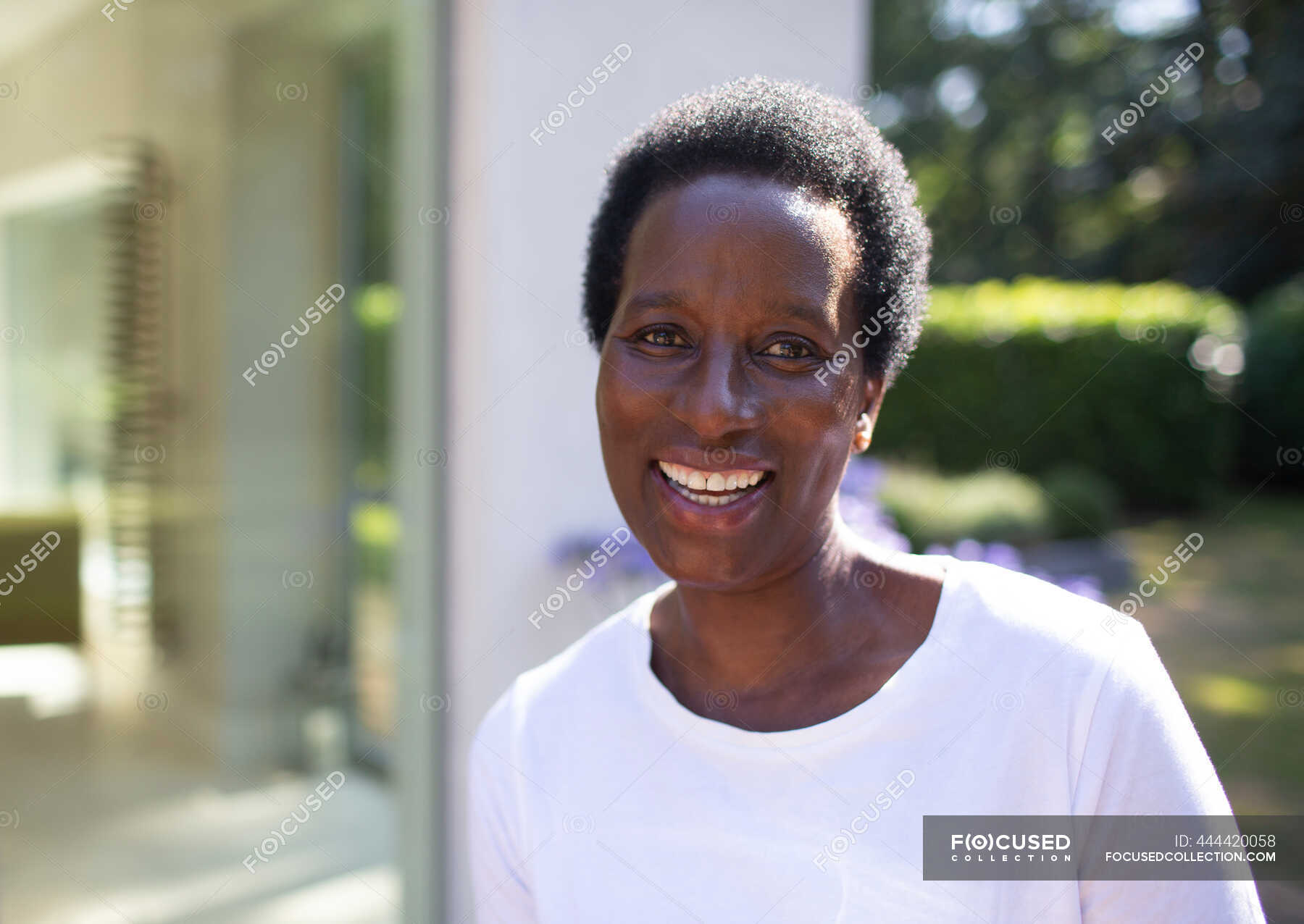 Portrait happy beautiful mature woman on sunny summer patio — wellbeing, looking at camera ...