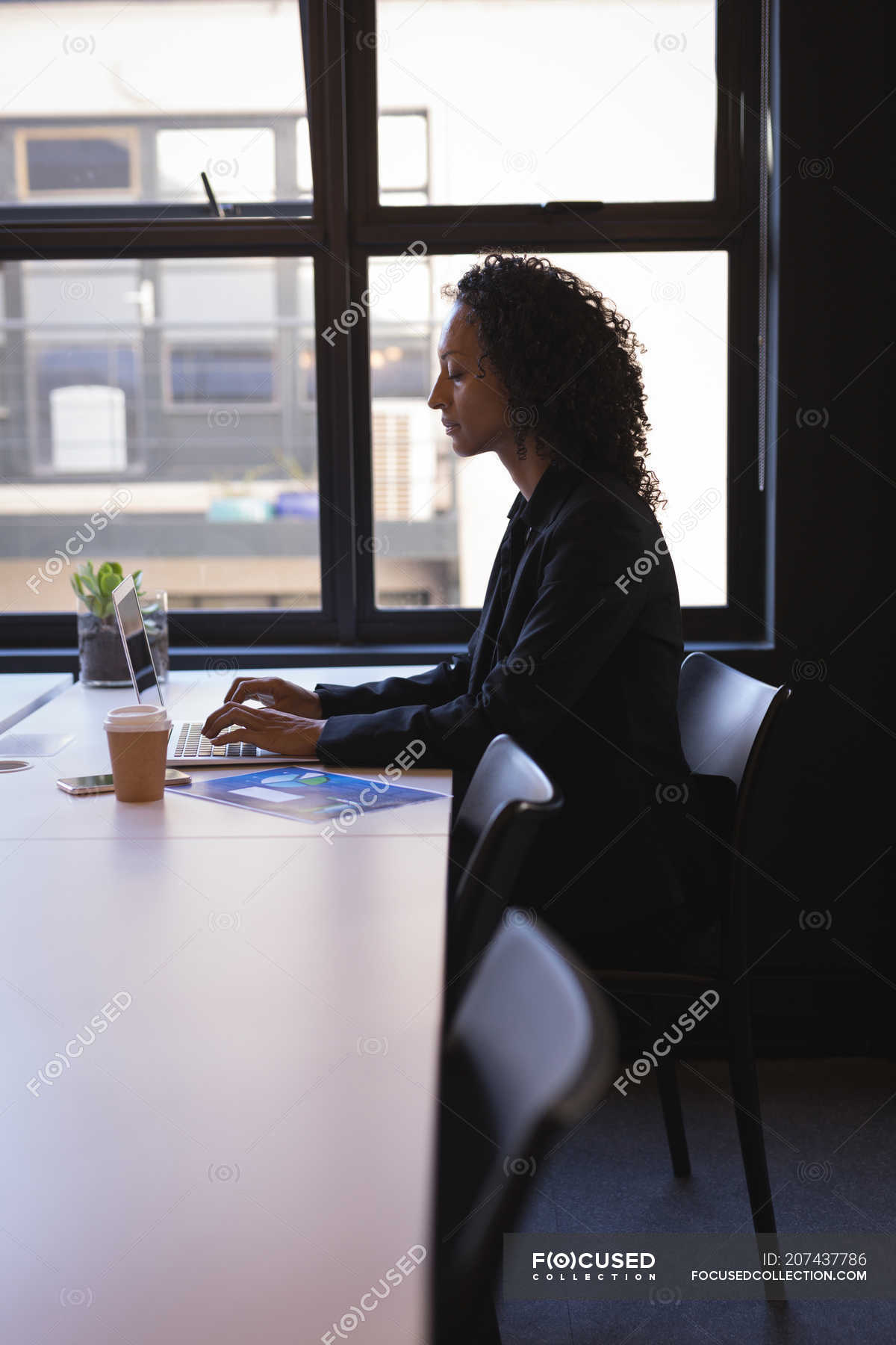 Side view of businesswoman sitting and using laptop at office cafeteria ...