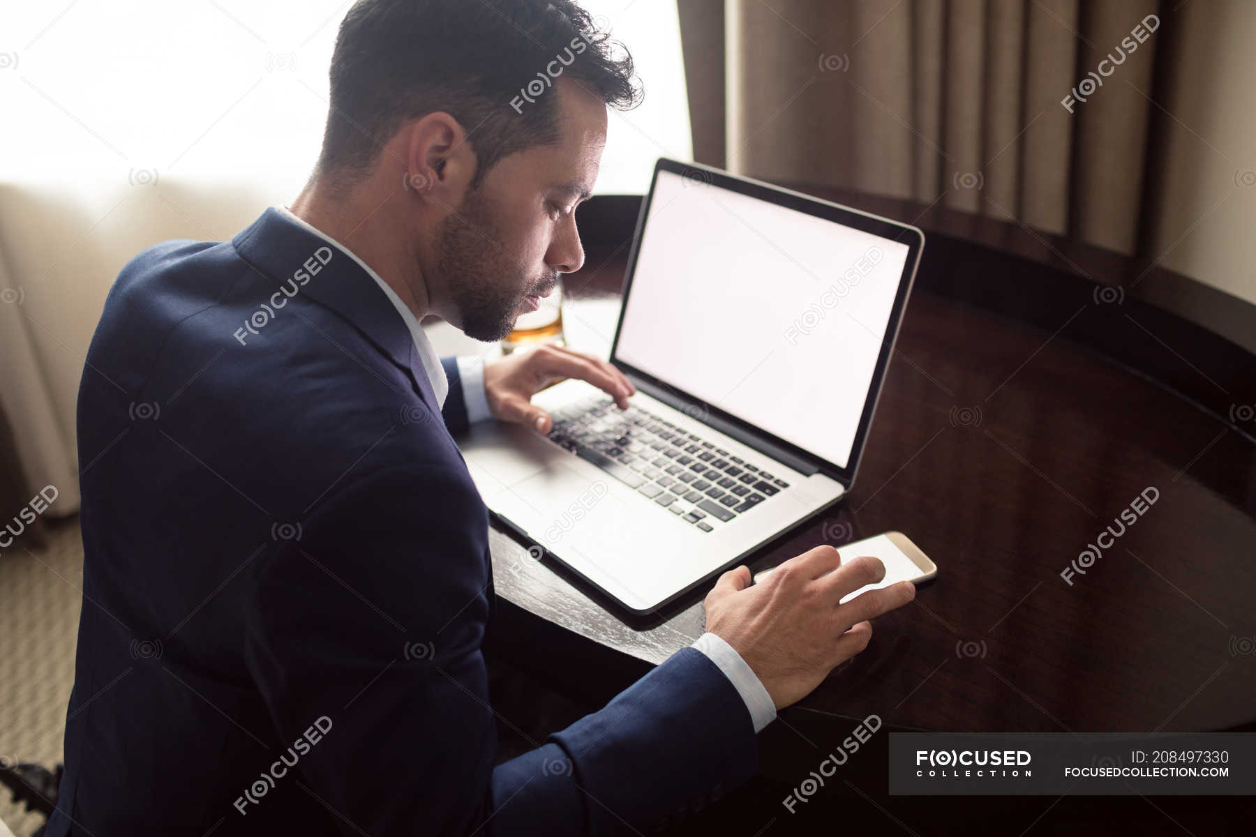 Businessman using mobile phone while working on laptop in hotel ... Businessman using mobile phone while working on laptop in hotel ...