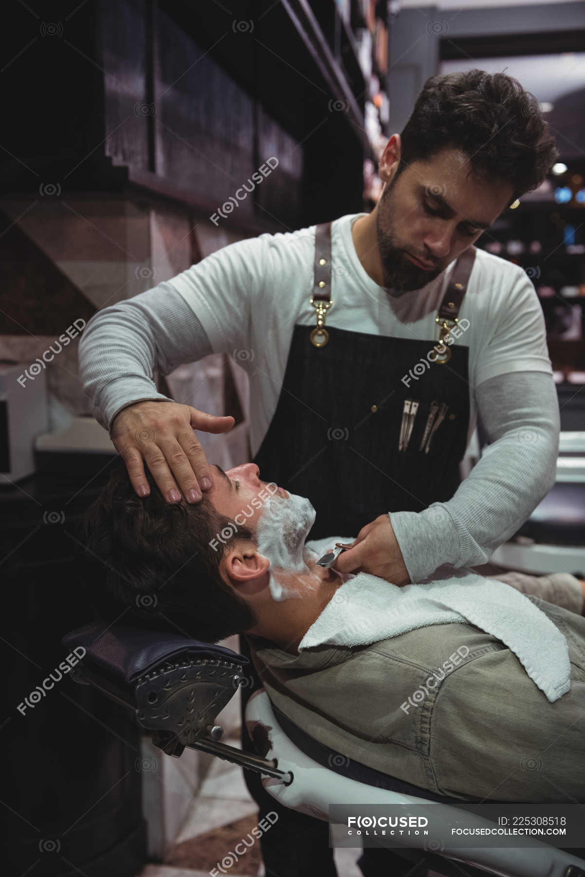 Man getting beard shaved by stylist with razor in barber shop ...