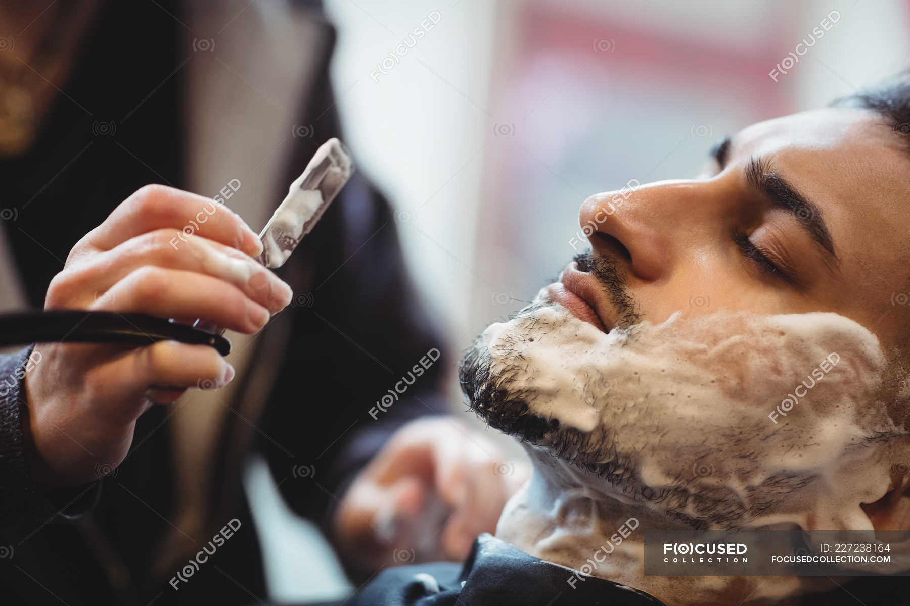 Man getting his beard shaved with razor in barber shop — stylist ...