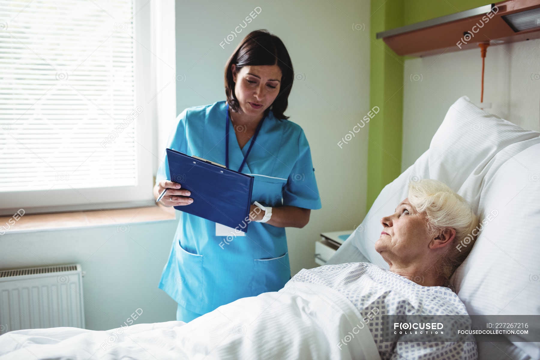 Nurse interacting over a report with senior patient in hospital ...