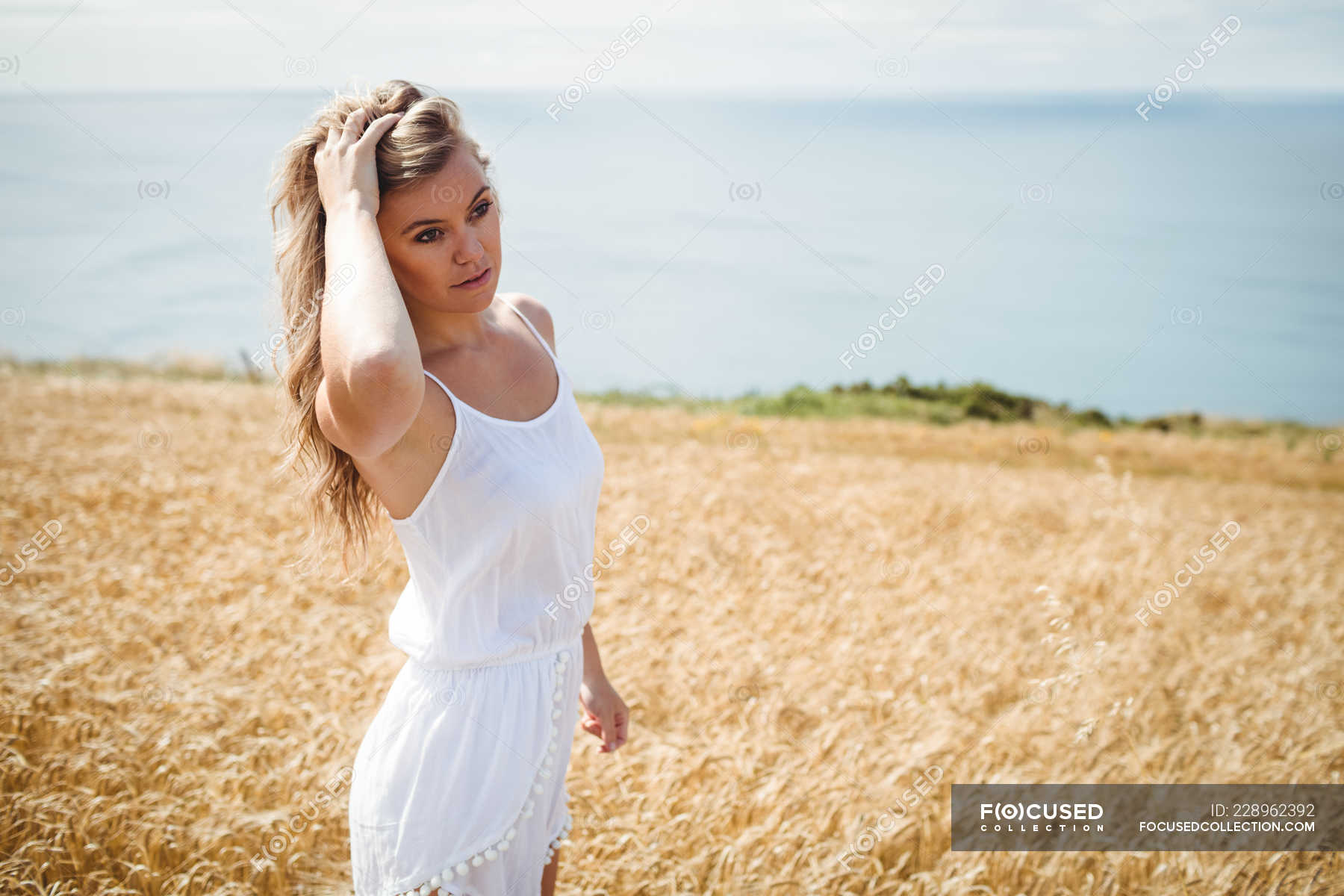 Woman with hand in hair standing in wheat field on sunny day ...