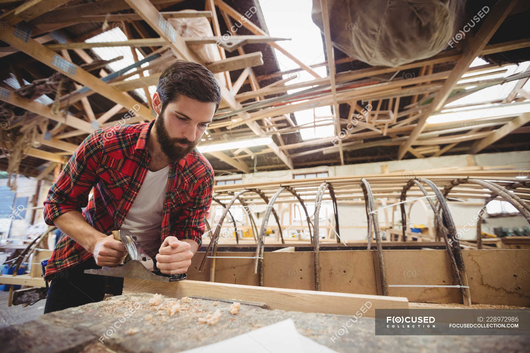 Man using hand plane to level the surface of the plank in boatyard ...