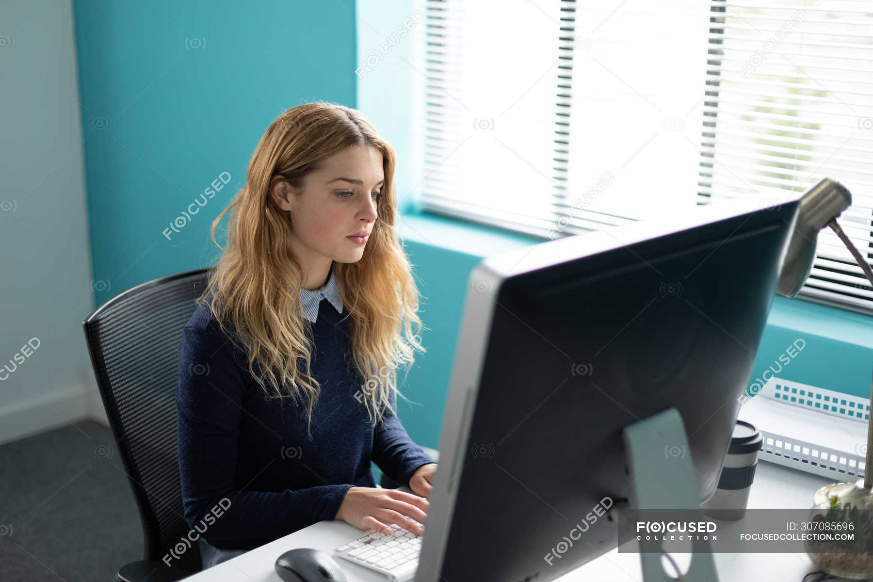 Side view of a young Caucasian woman sitting at a desk by a window ...
