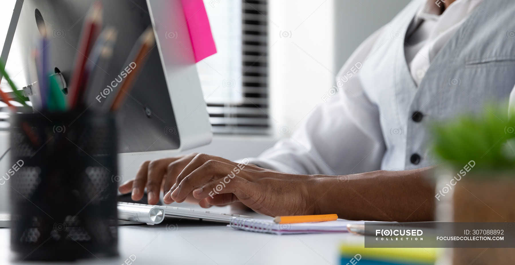 Side view mid section of man sitting at a desk using a computer in the ...