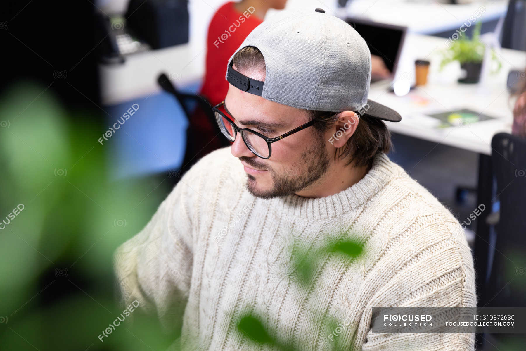 Side view of a young Caucasian man sitting at a desk using a computer ...