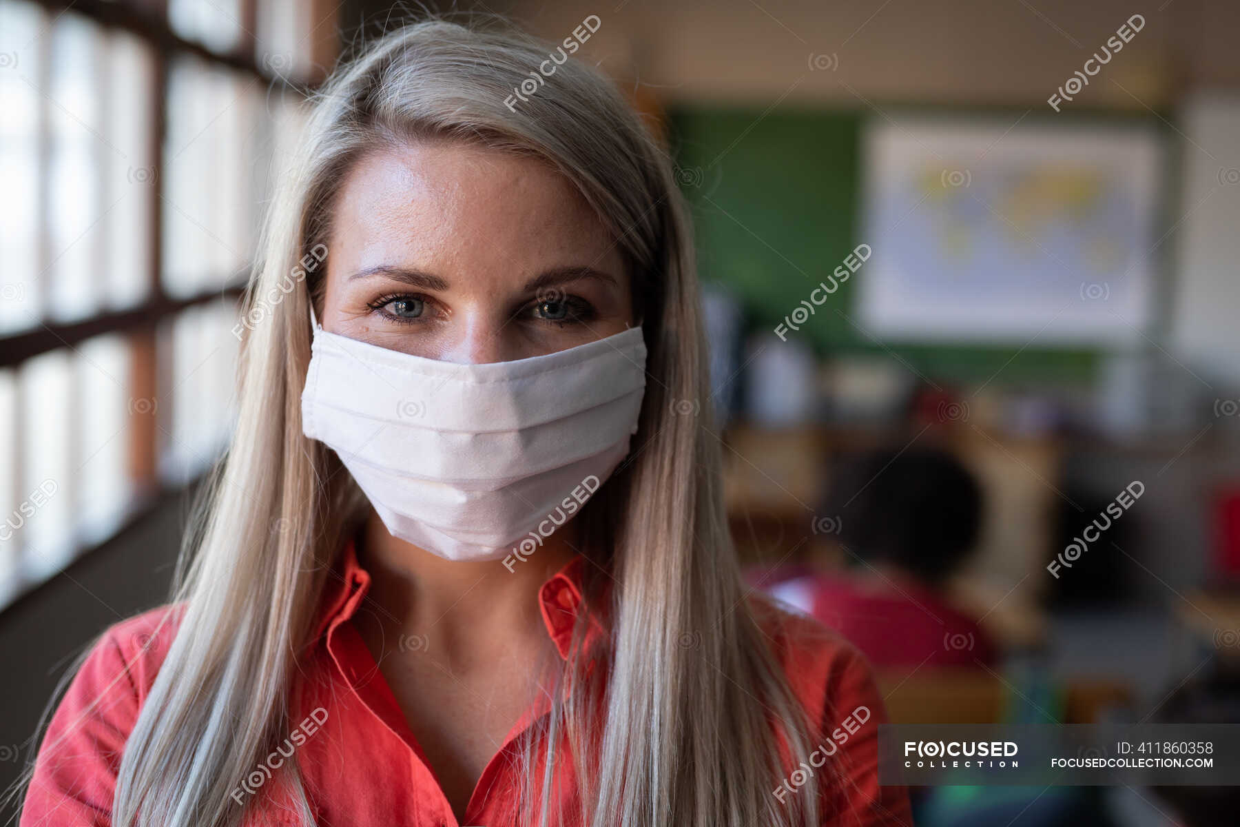 Portrait of a female Caucasian teacher wearing face mask in classroom ...