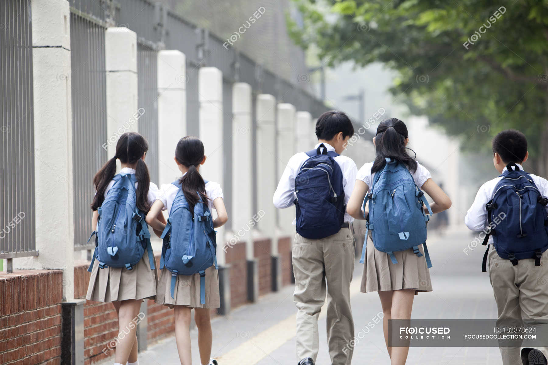 Rear view of schoolchildren in school uniform walking at sidewalk ... Rear view of schoolchildren in school uniform walking at sidewalk ...