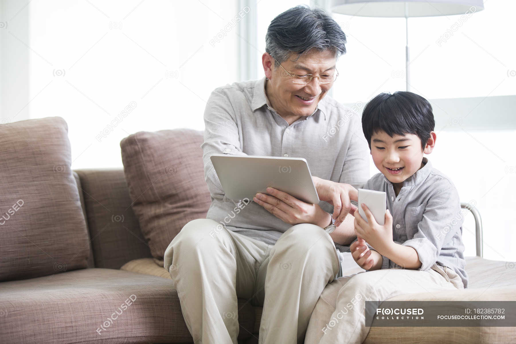 Chinese grandfather and grandson using digital tablet and smartphone on ... Chinese grandfather and grandson using digital tablet and smartphone on ...