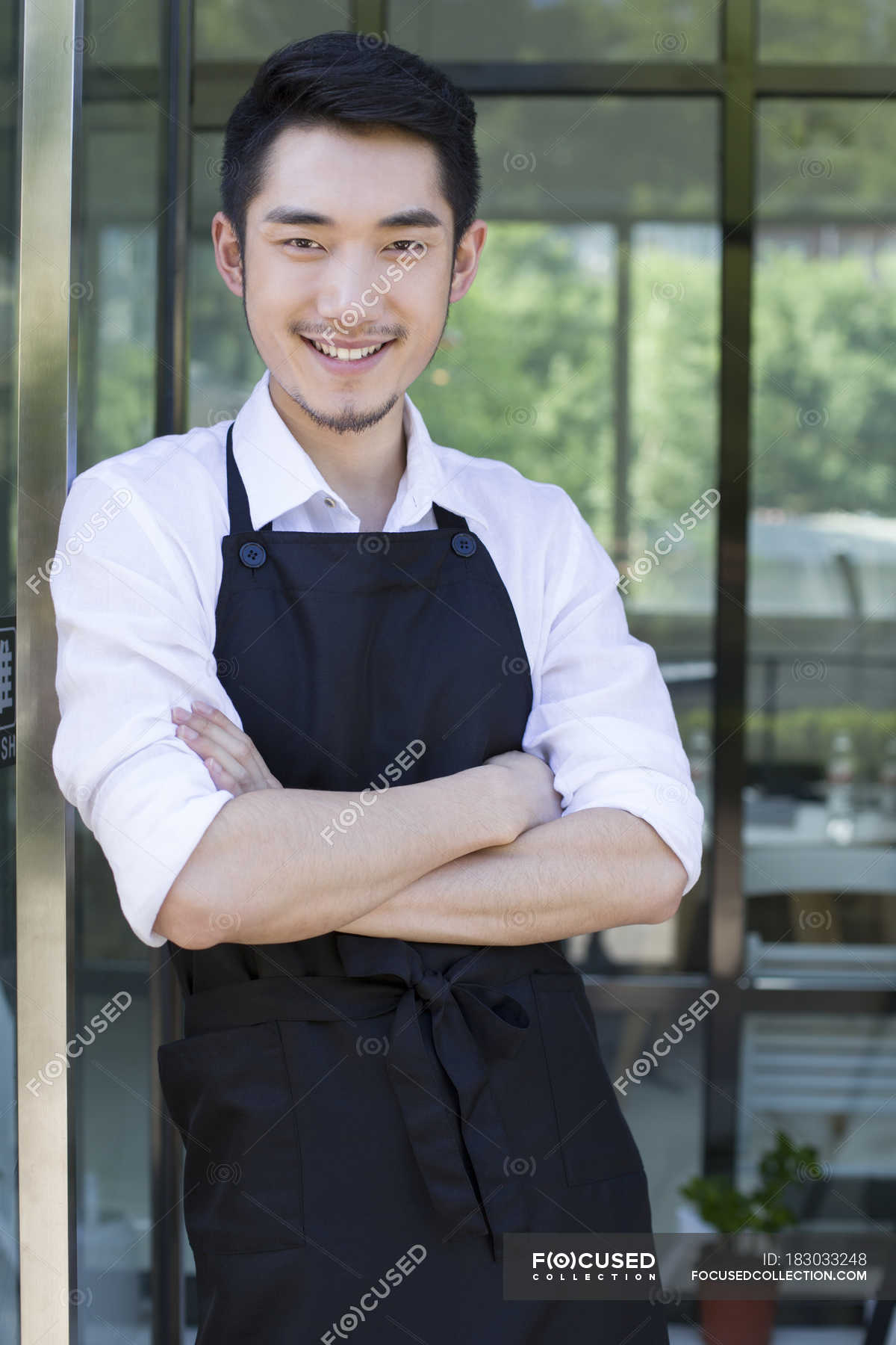 Shopkeeper Standing In Doorway Of Coffee Shop With Arms Folded shopkeeper-standing-in-doorway-of-coffee-shop-with-arms-folded
