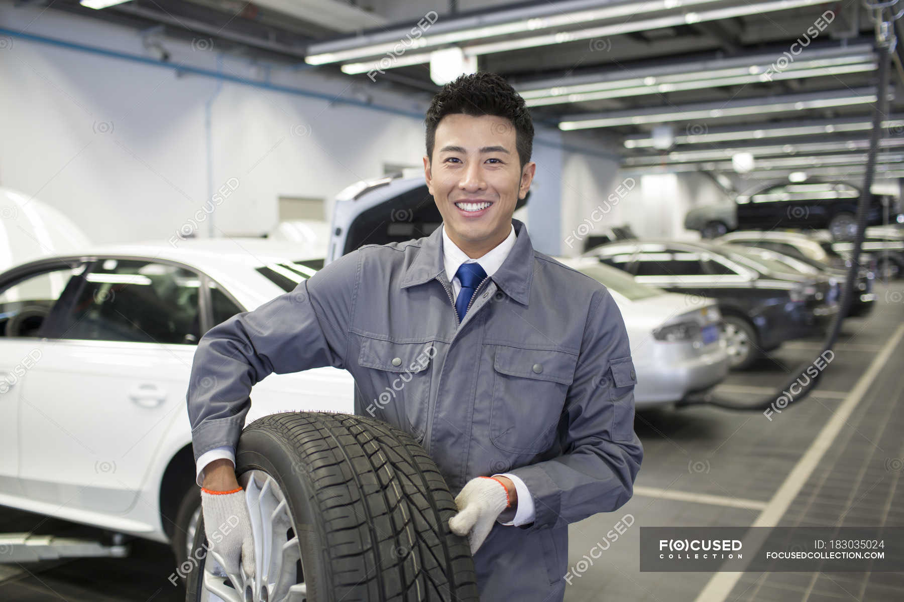Chinese auto mechanic holding car wheel in workshop — man, uniform - Stock Photo | #183035024