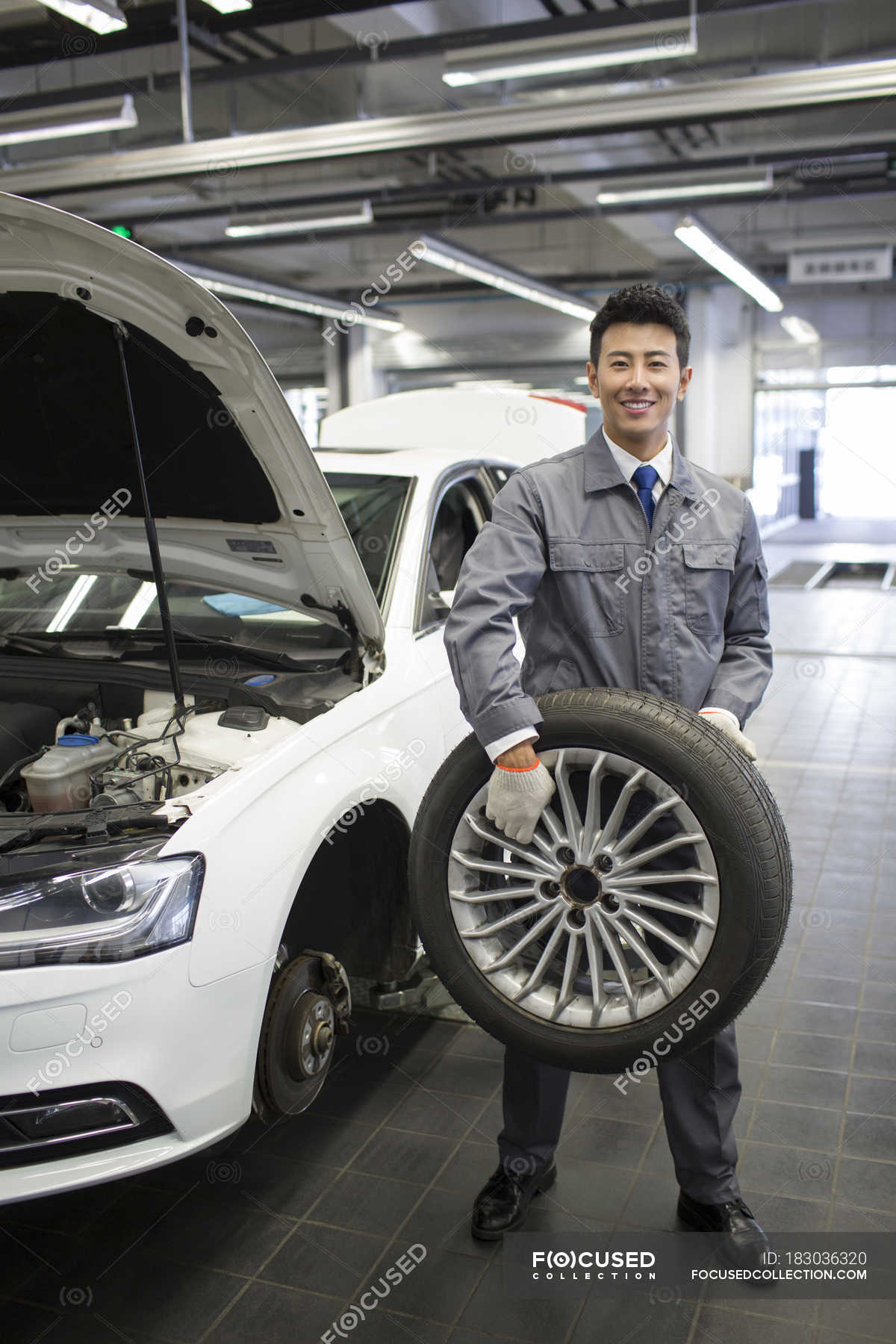 Chinese auto mechanic holding car wheel in workshop — occupation, smiling - Stock Photo | #183036320
