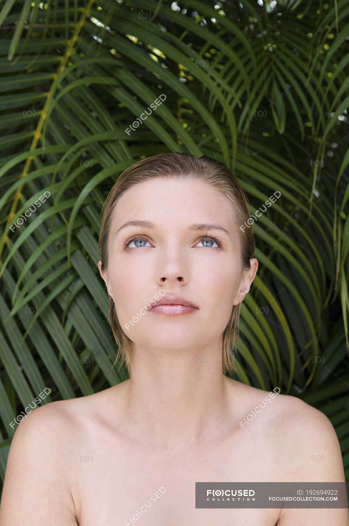 Young Woman With Bare Shoulders Looking Up With Tropical Plants In
