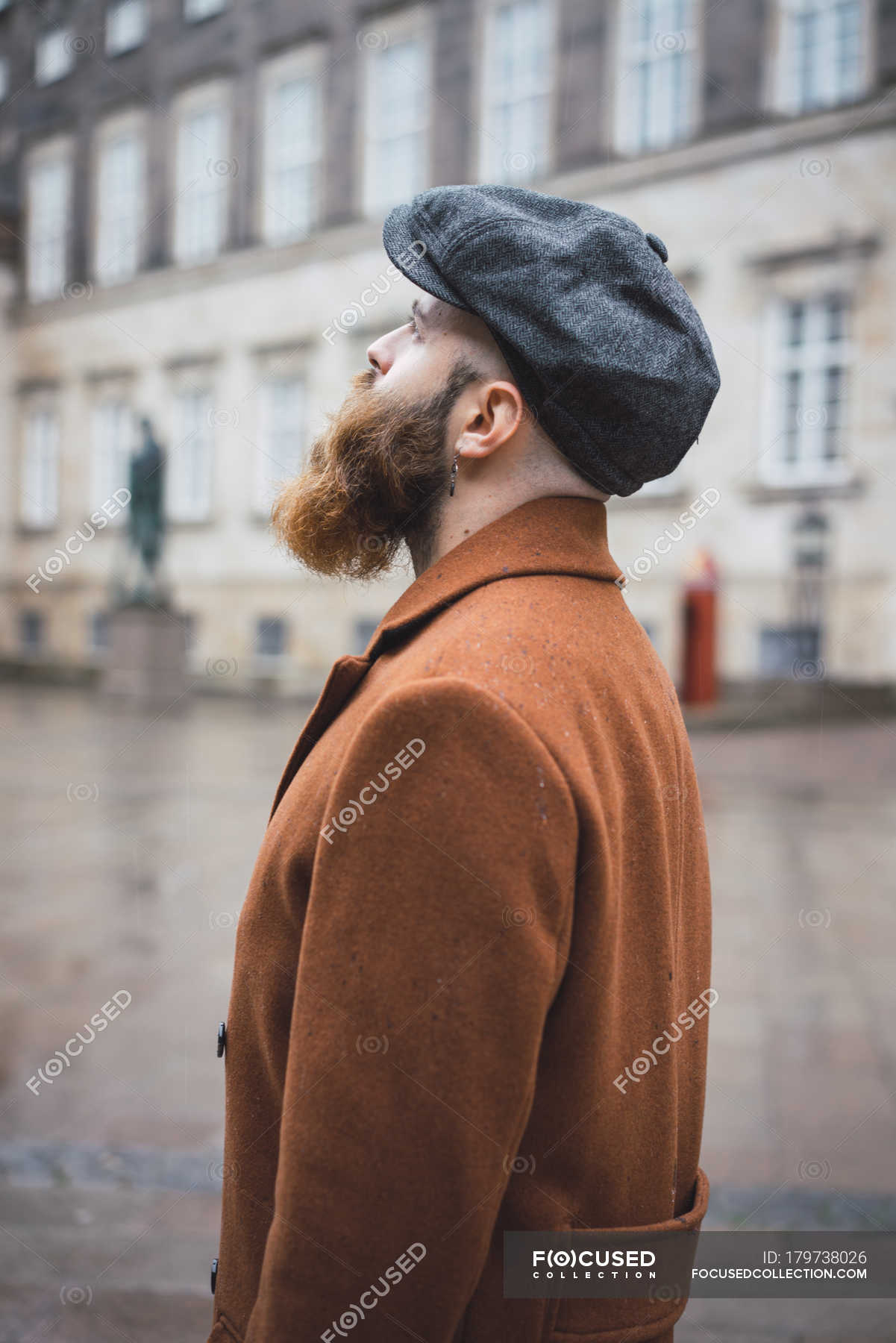 Side view of bearded man in posing in coat and cap and looking up ...