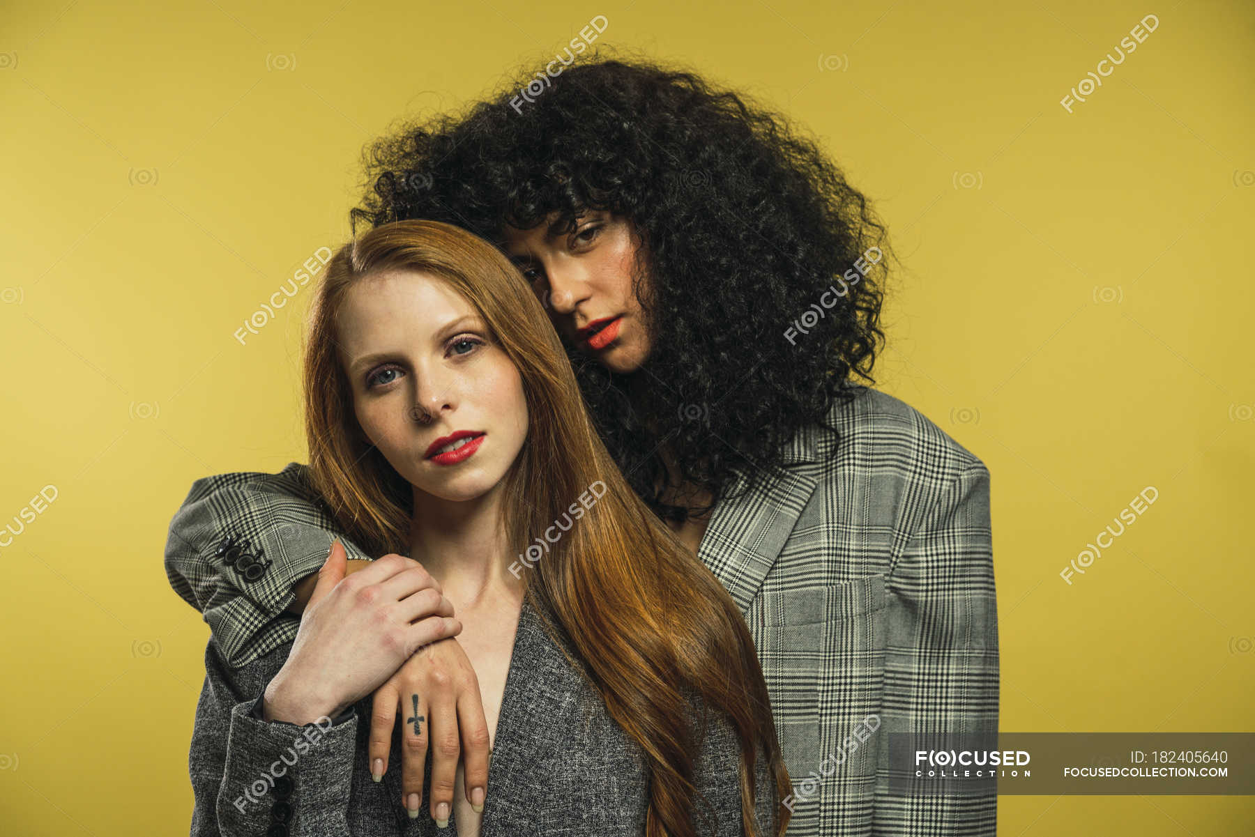 Two women embracing and looking at camera on yellow background ...