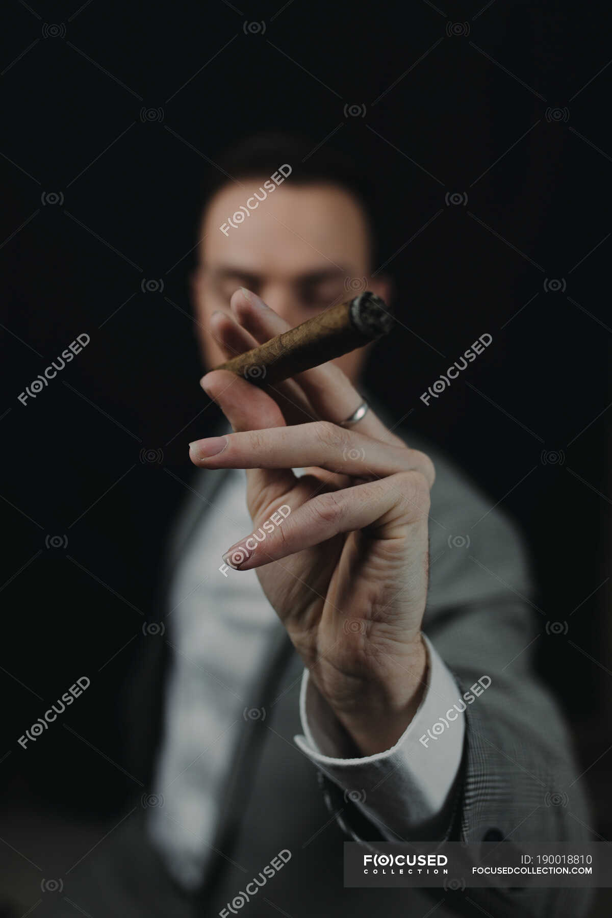 Close-up hand of handsome man in suit smoking cigar on dark background. — businessman, confident ...