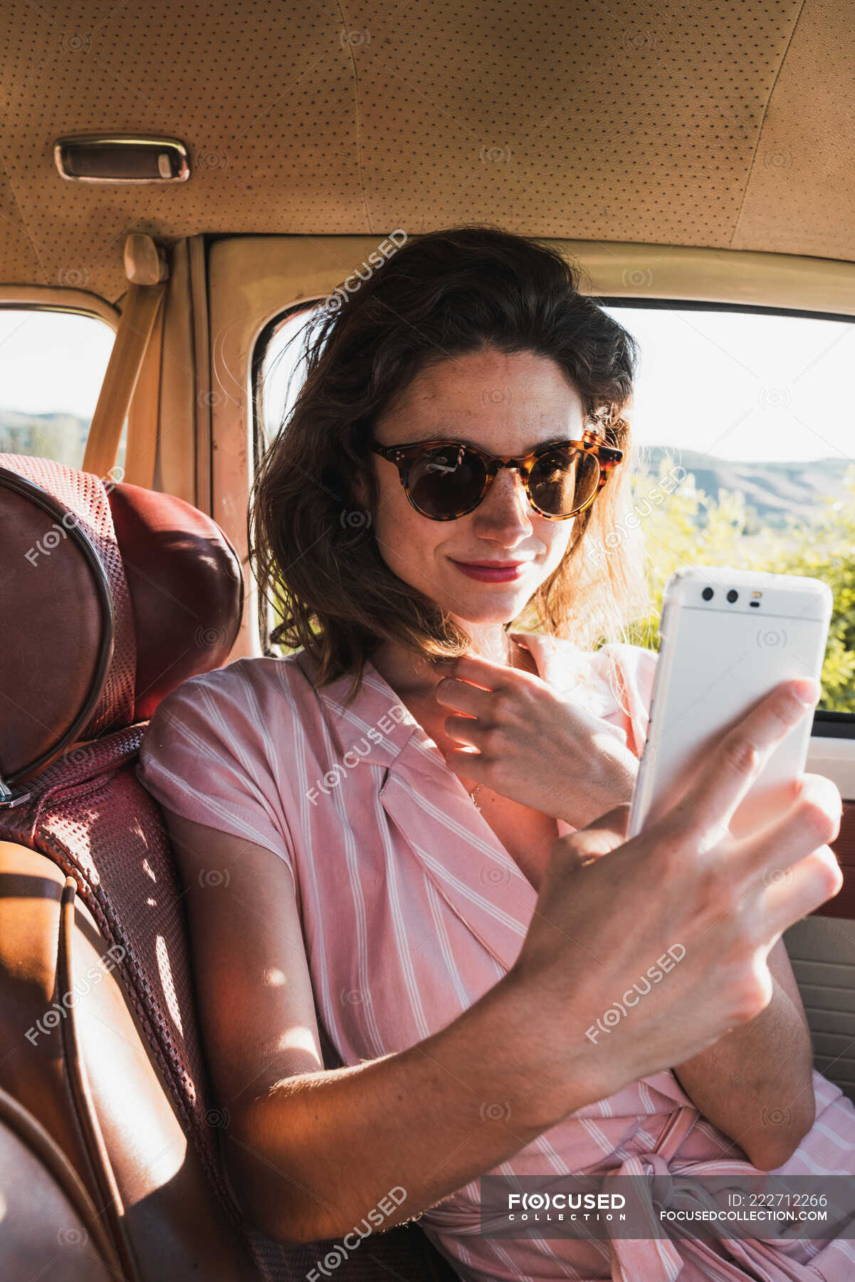 Beautiful brunette in pink dress and trendy sunglasses using phone and ...