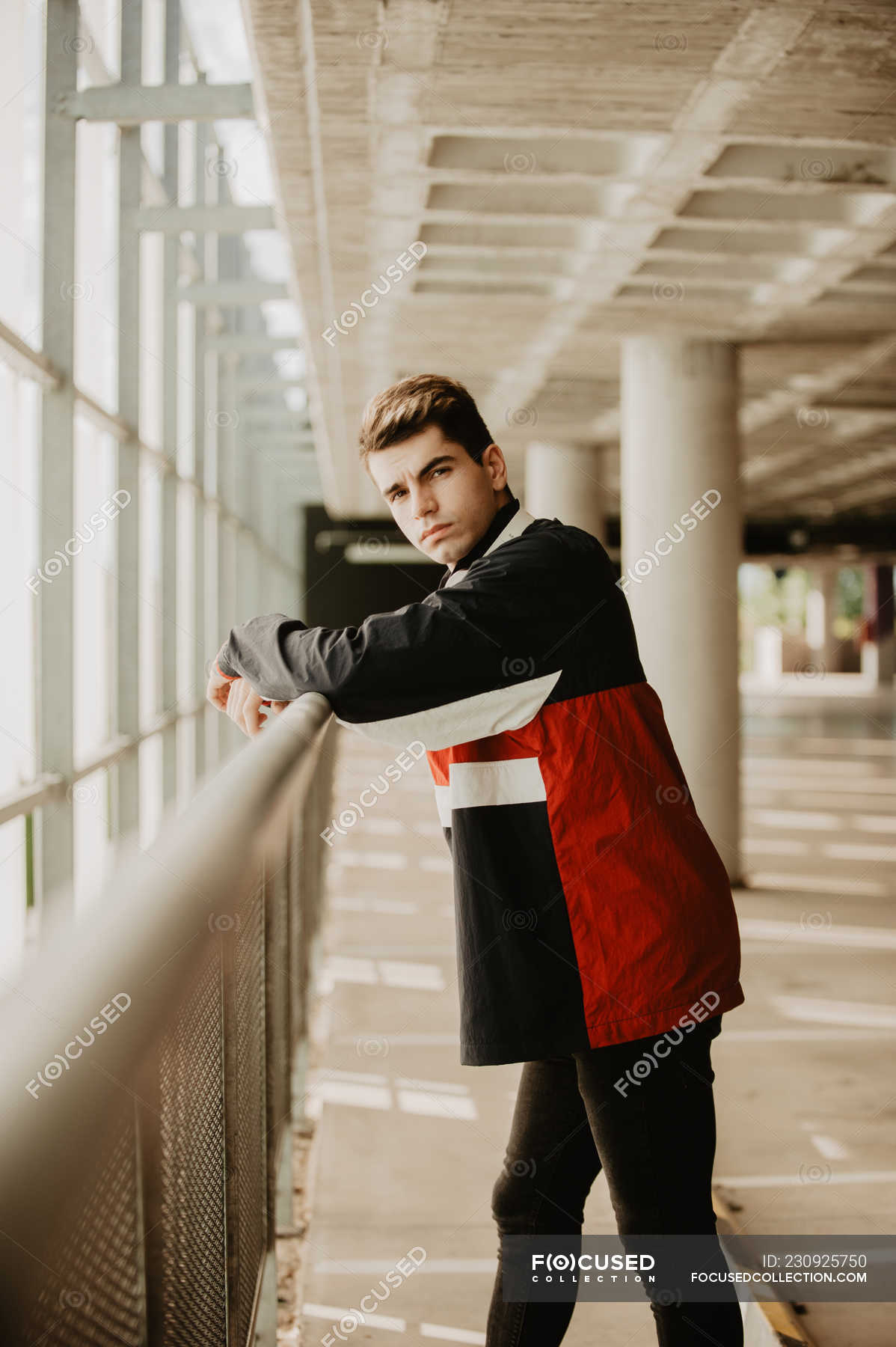 Young thoughtful man standing inside building and leaning on railing ...