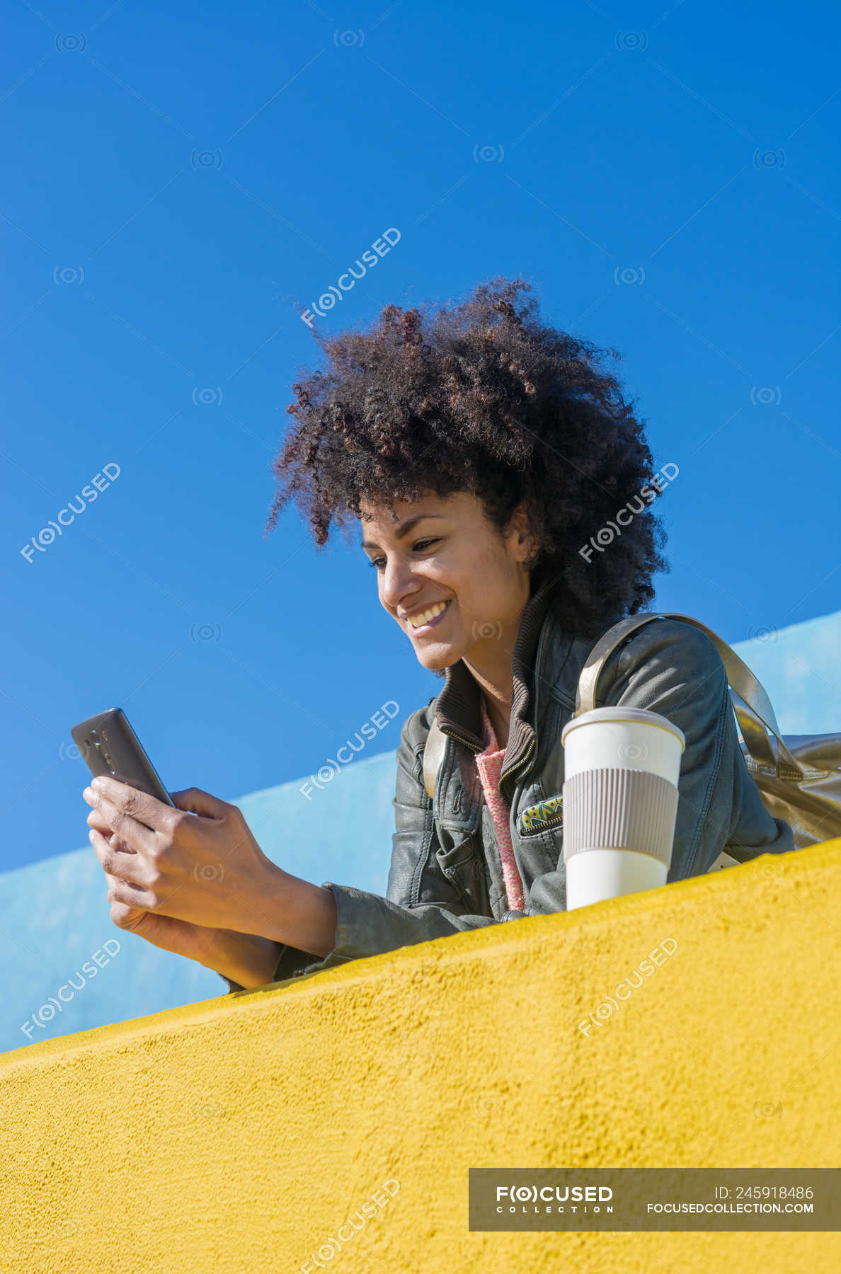 Black Woman With Afro Hair Leaning Against Brightly Colored Walls While