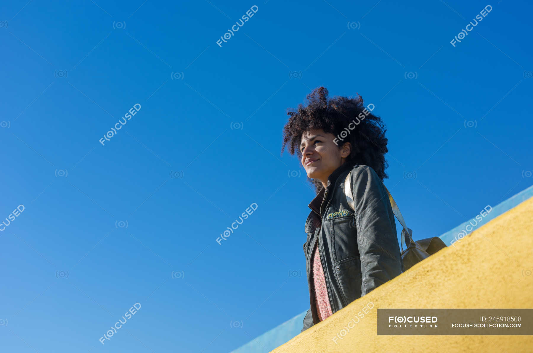 Black Woman With Afro Hair Leaning Against Brightly Colored Walls While