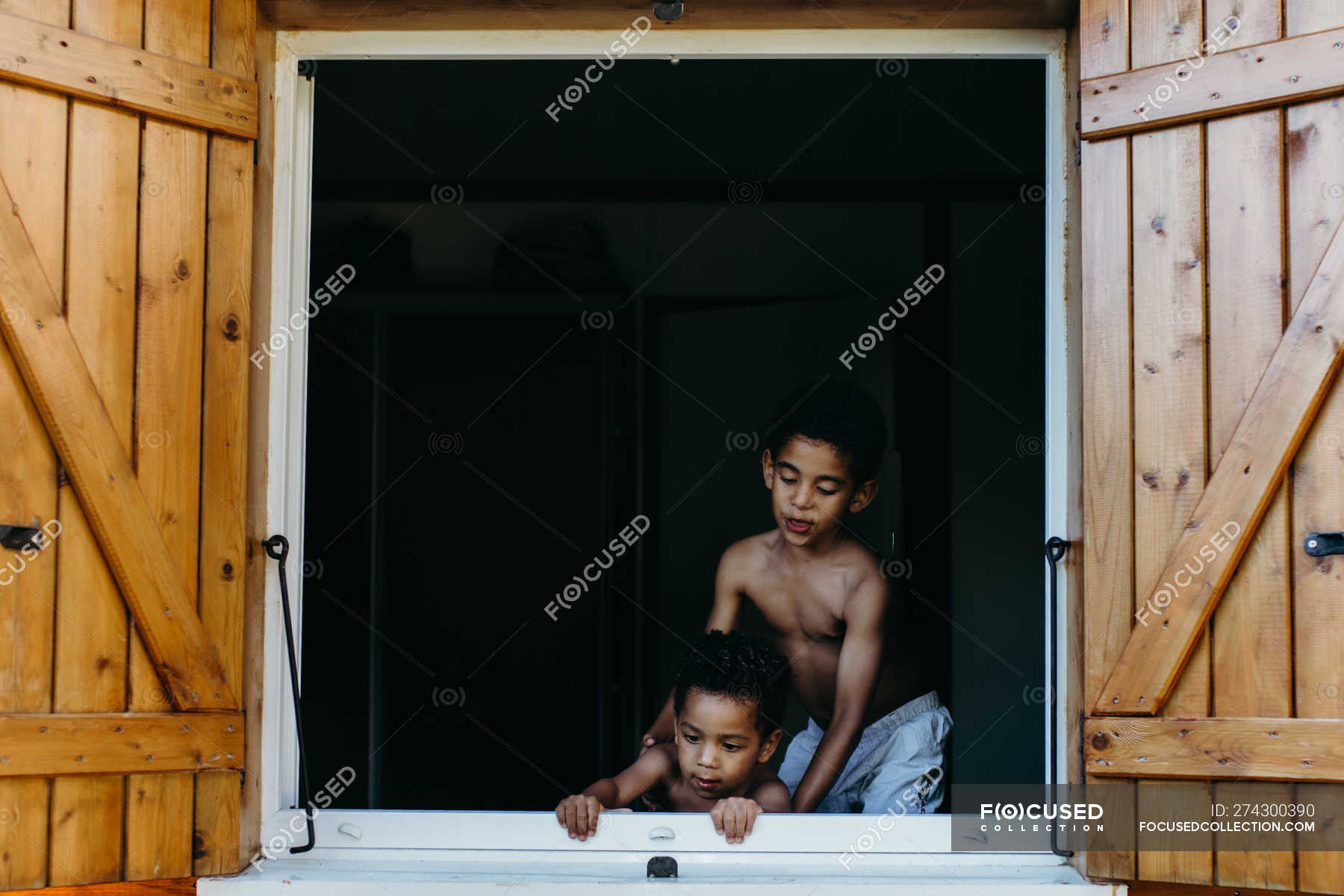 Two shirtless African American brothers looking out open window of ... Two shirtless African American brothers looking out open window of ...
