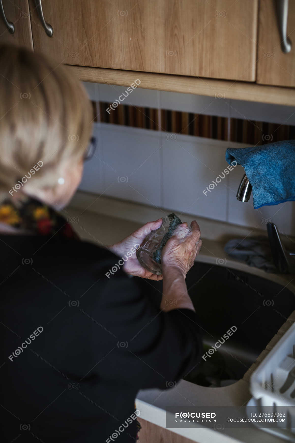 Back View Of Elderly Woman Standing Near Sink And Washing Glass With