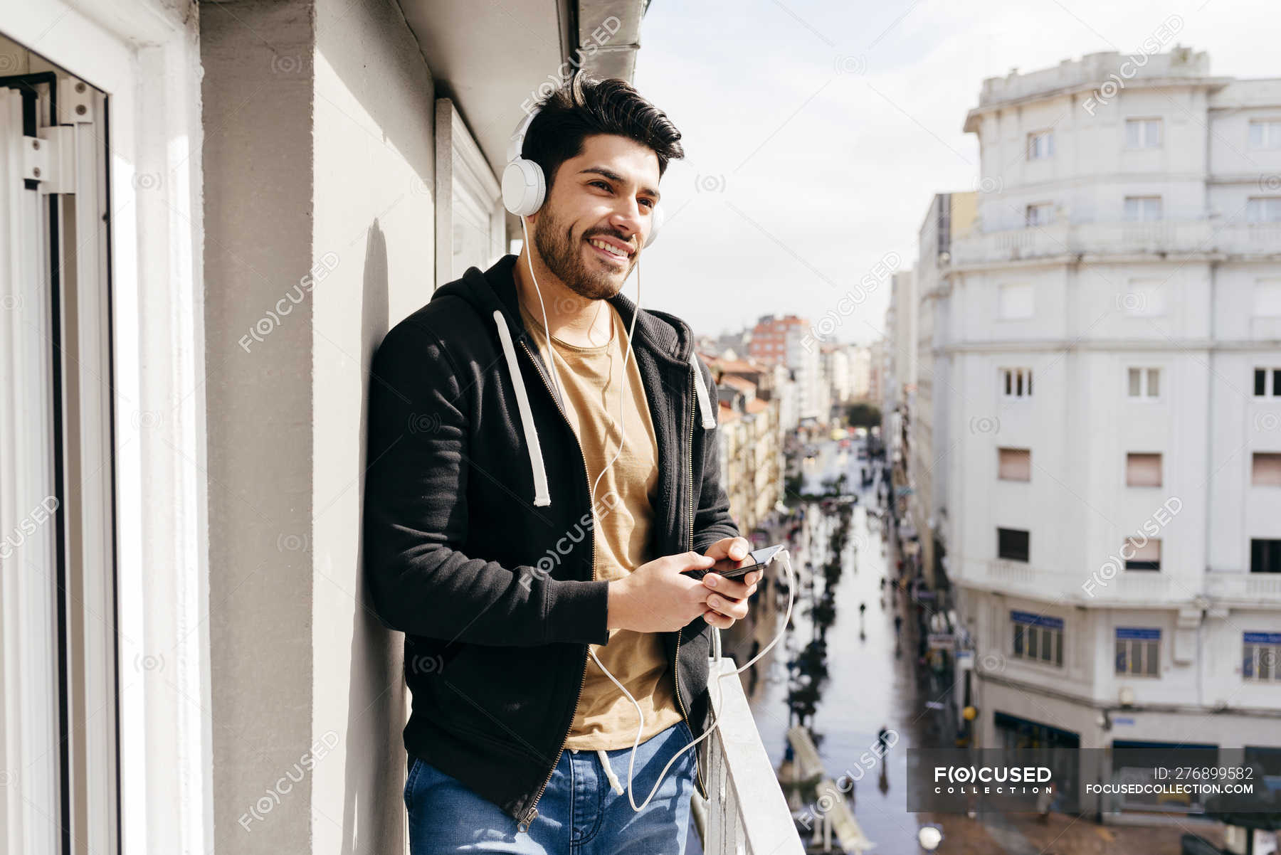 Young smiling handsome casual male in headset leaning on terrace ...