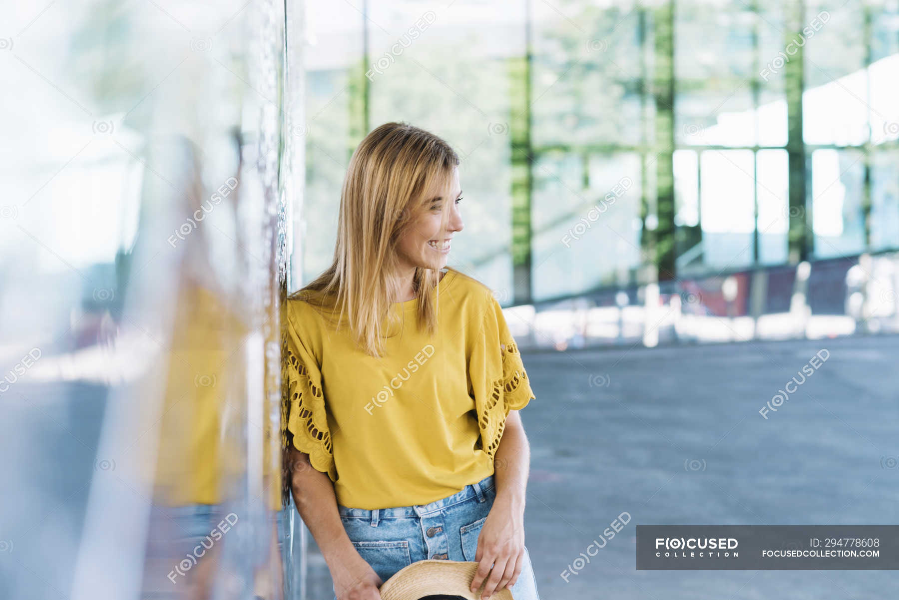 Young blonde woman leaning on wall and looking away, holding a straw ...