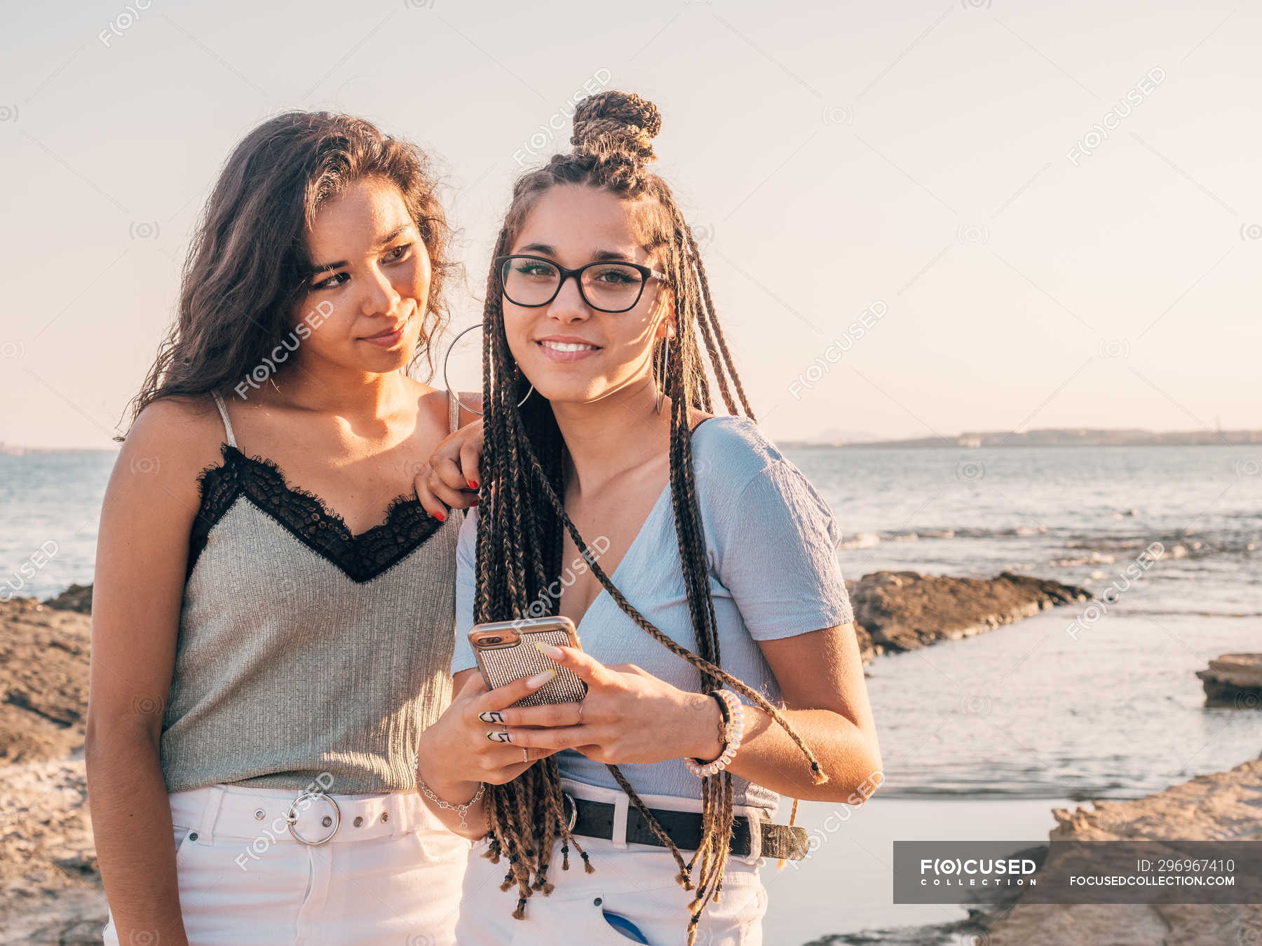 Smiling trendy young women using smartphone on beach — horizontal ... Smiling trendy young women using smartphone on beach — horizontal ...