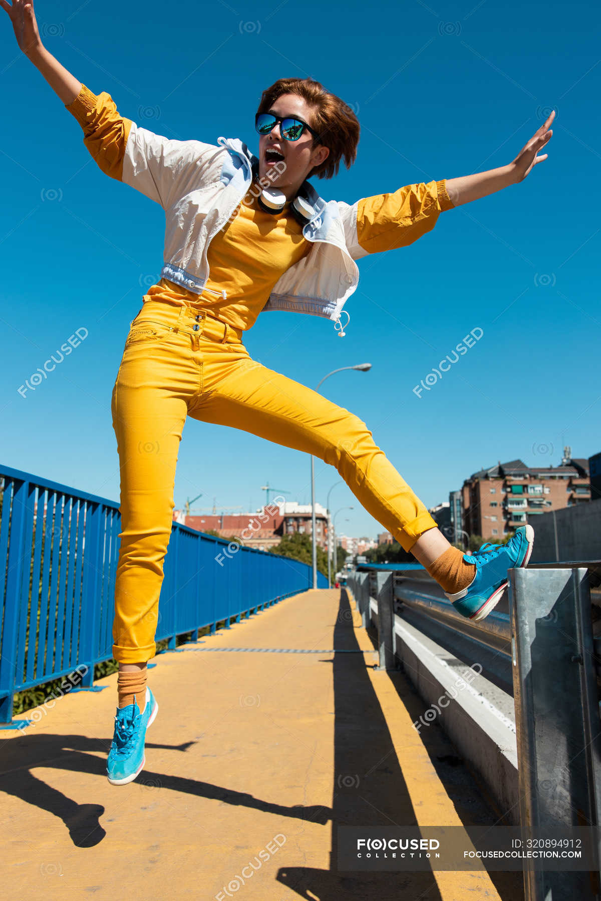 From Below Cheerful Courageous Teenager In Sunglasses Jumping With Mouth Open And Arms Raised On