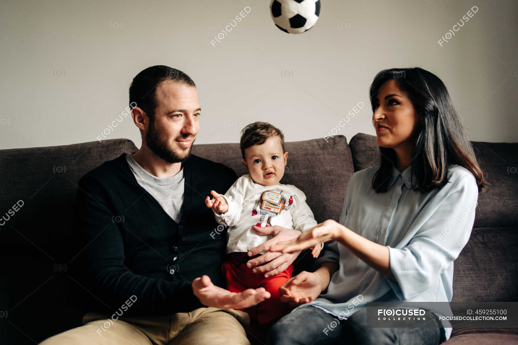 Loving young parents sitting on couch and and hugging cute little son playing with ball at home ...